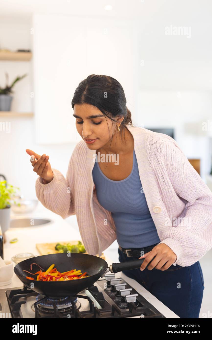 Asian woman cooking vegetables in kitchen, enjoying aroma while ...