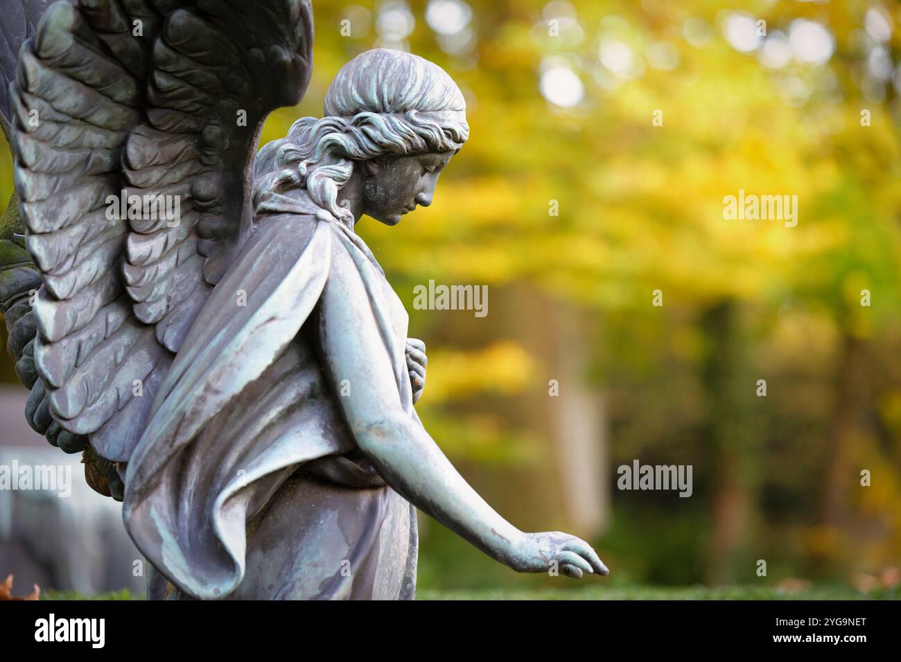 a winged angel figure in profile in an autumnal cemetery looks sadly to ...