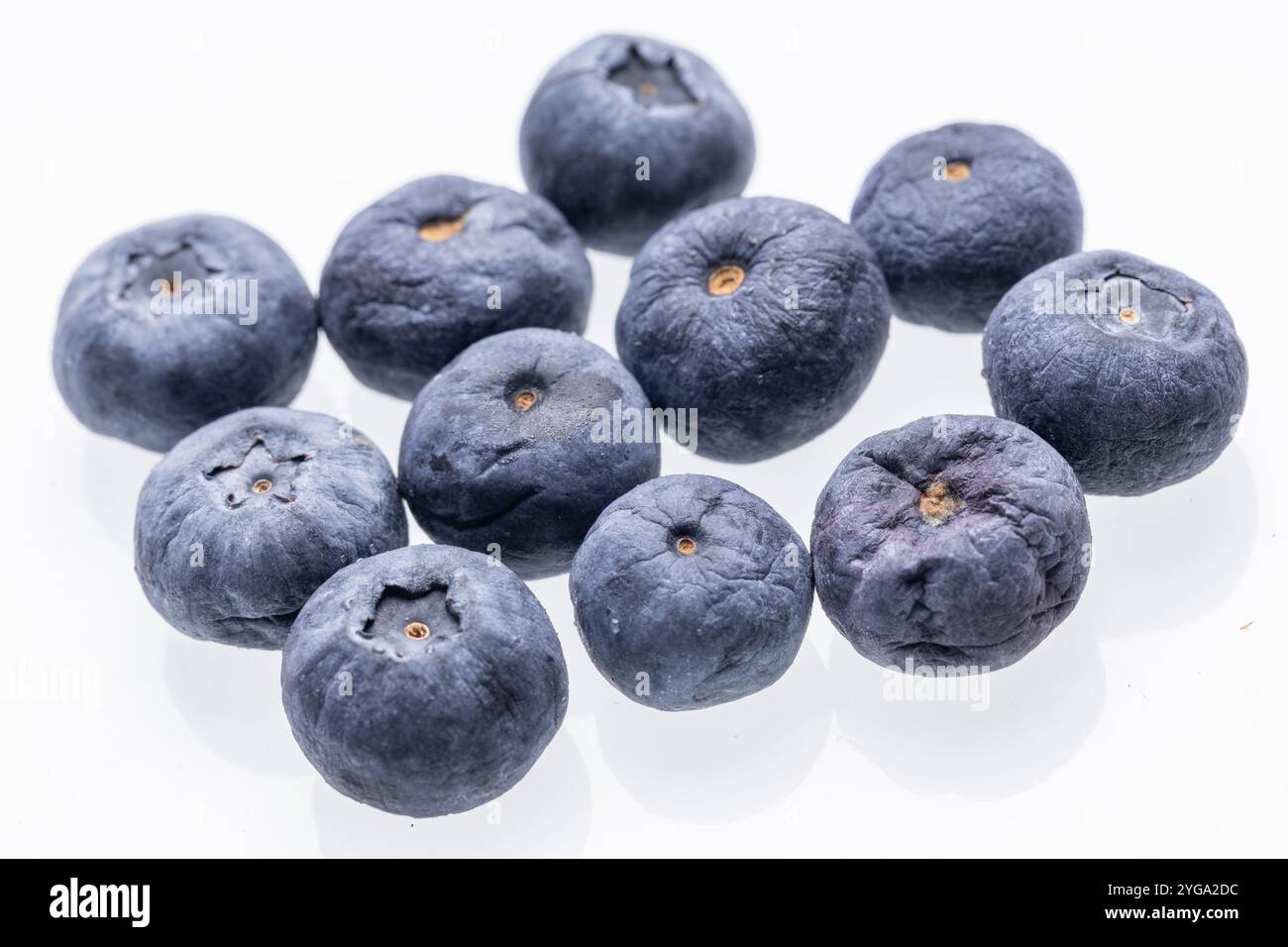 Ten blueberries with wrinkled skin are scattered on a white surface ...