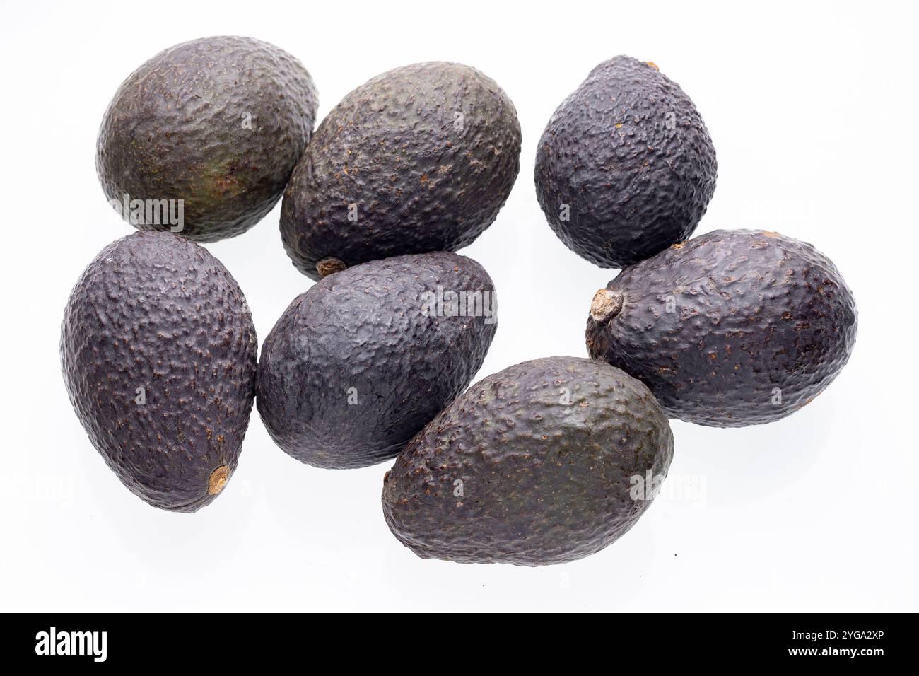 Seven whole ripe avocados with brown skin are arranged in a circle on a ...