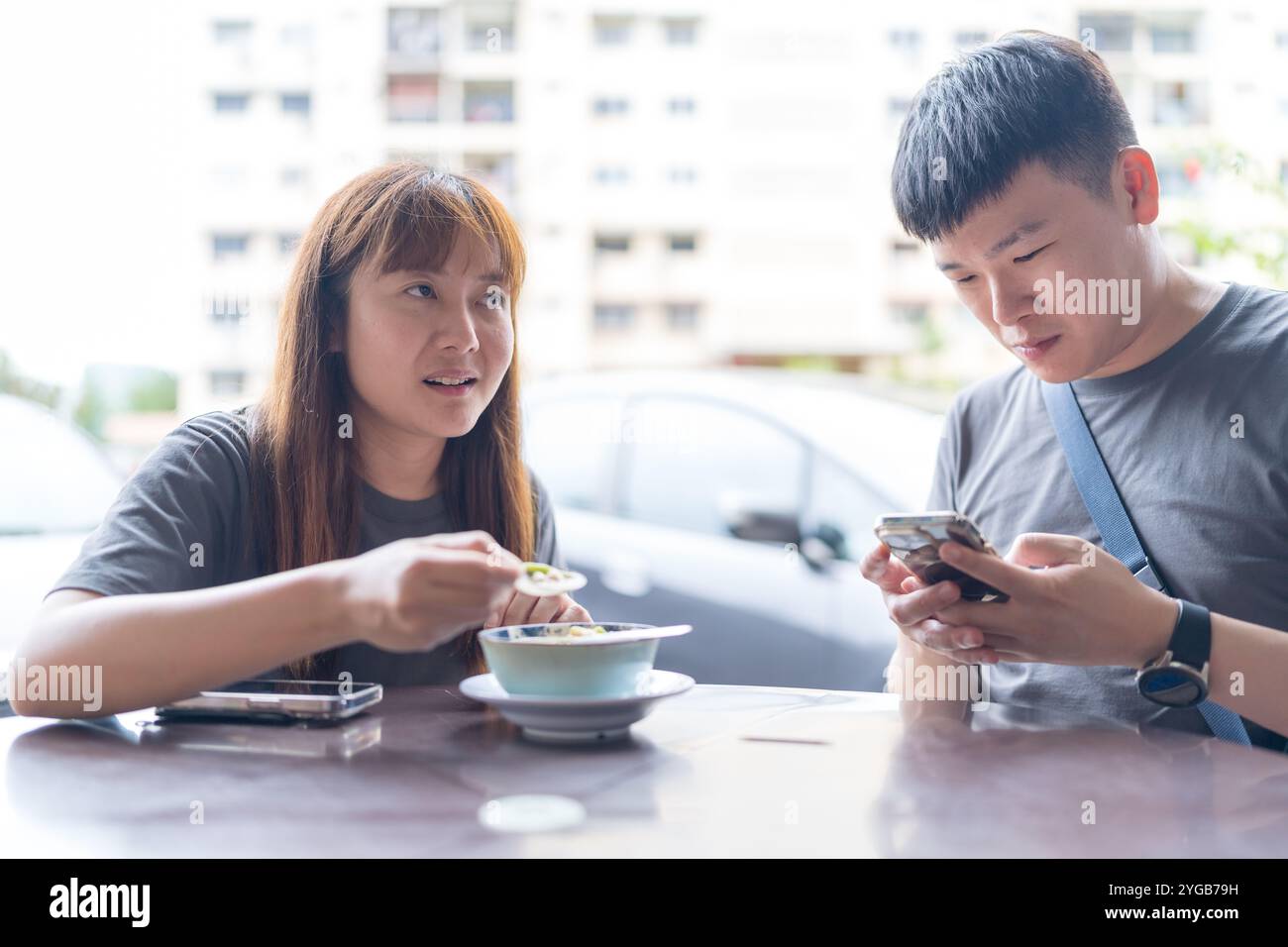 June 2024. A Chinese-Malaysian couple in their 30s chat while eating ...