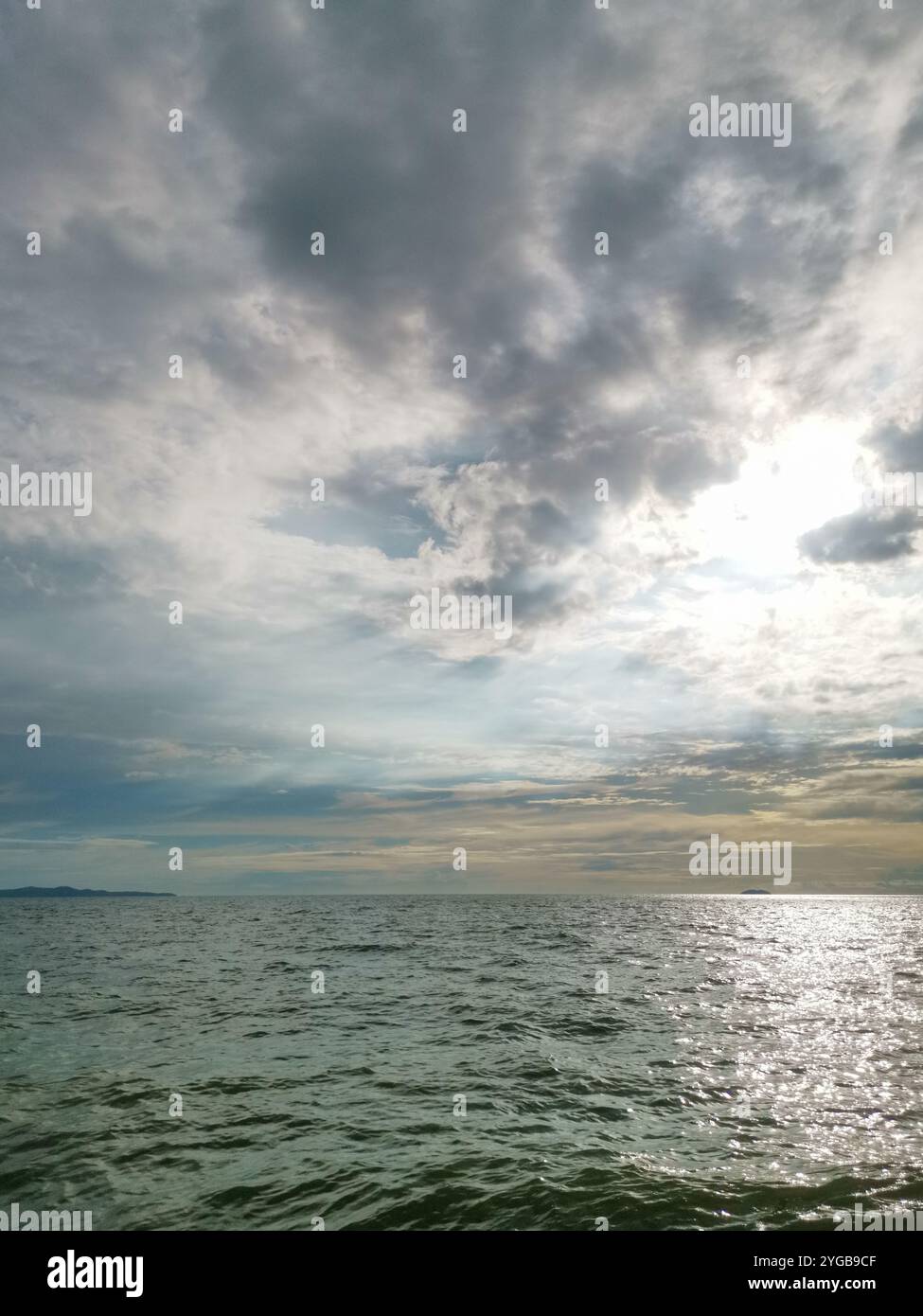 The sky is cloudy and the ocean is calm. The sun is shining through the ...
