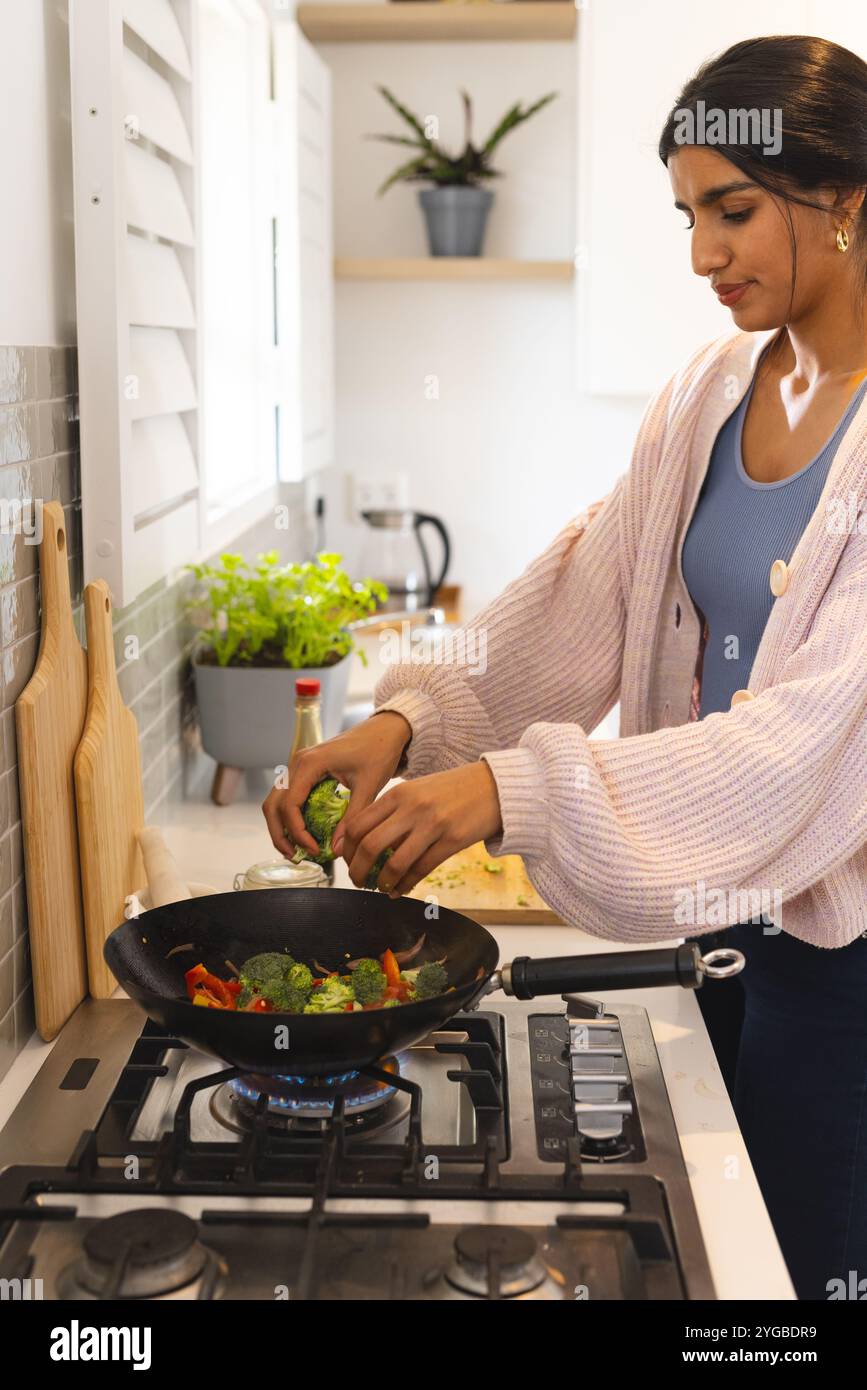Asian woman cooking vegetables in kitchen, adding fresh ingredients to ...