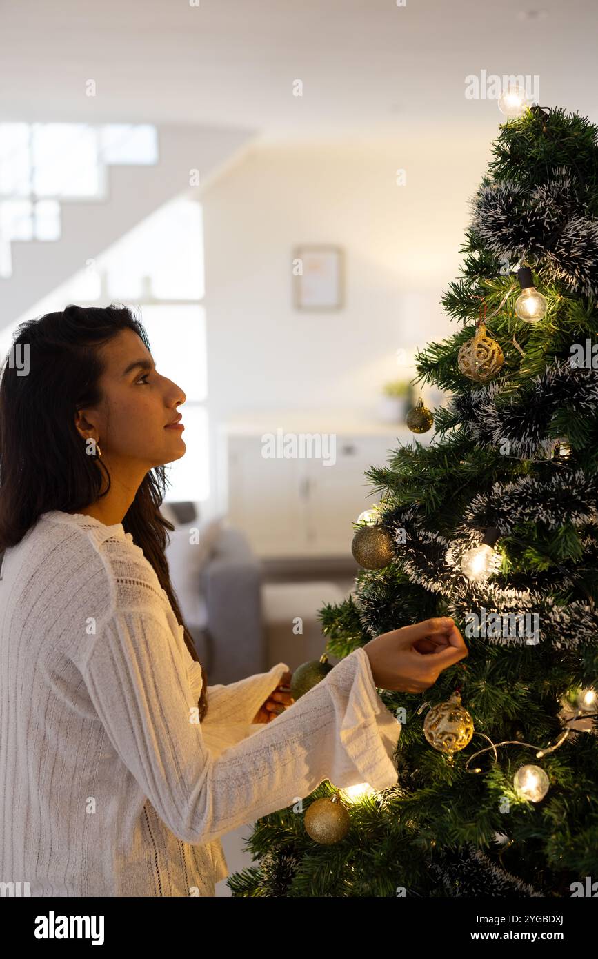 Decorating Christmas tree, Asian woman admiring ornaments at home ...