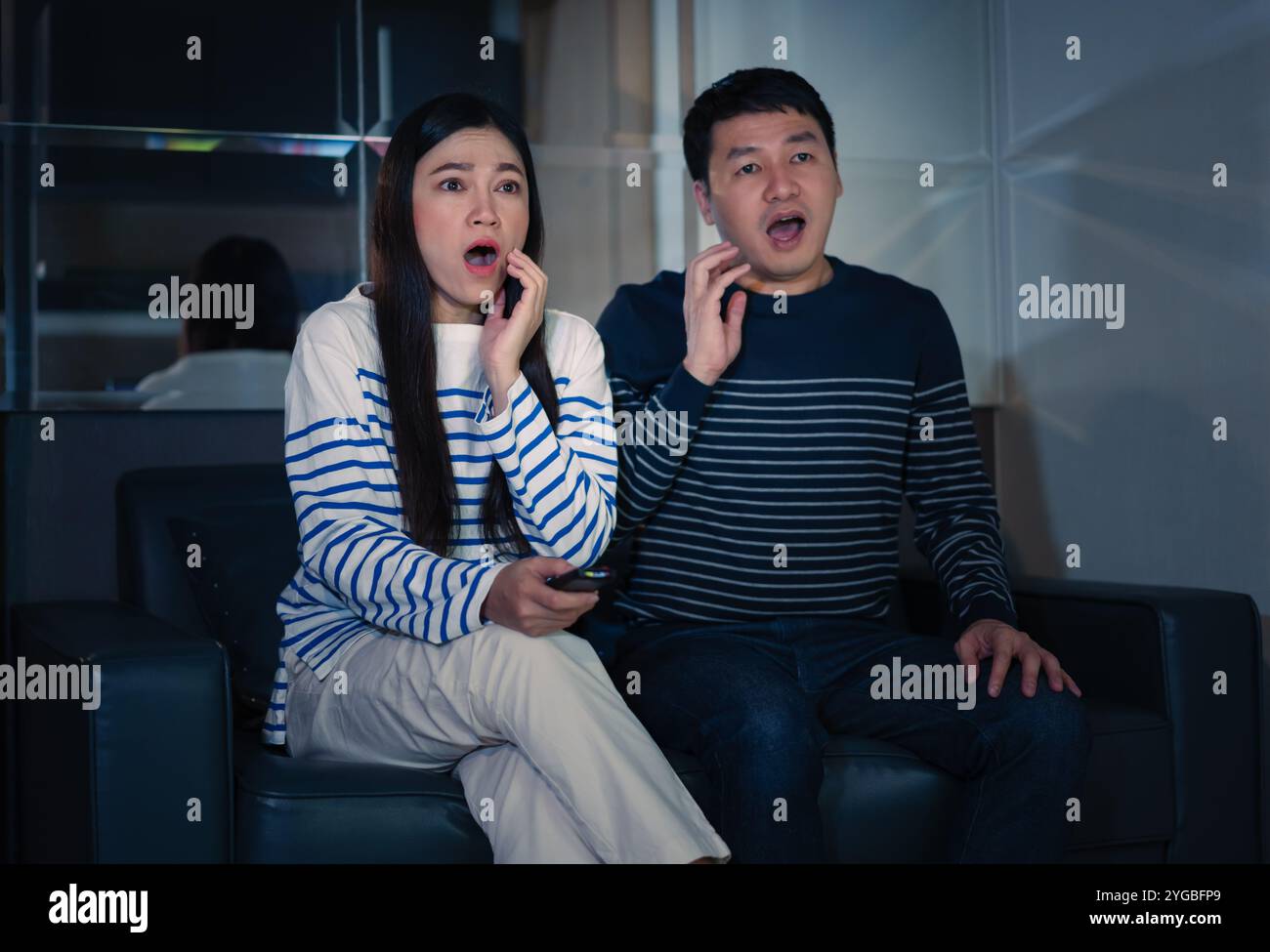 shocked and scared couple is watching horror movie TV on a sofa at ...