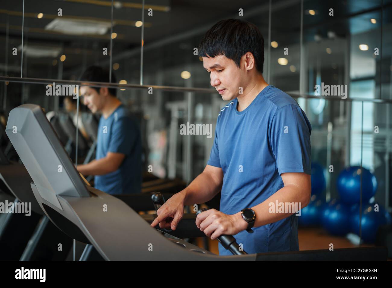 young man pushing start running button on treadmill at fitness gym ...