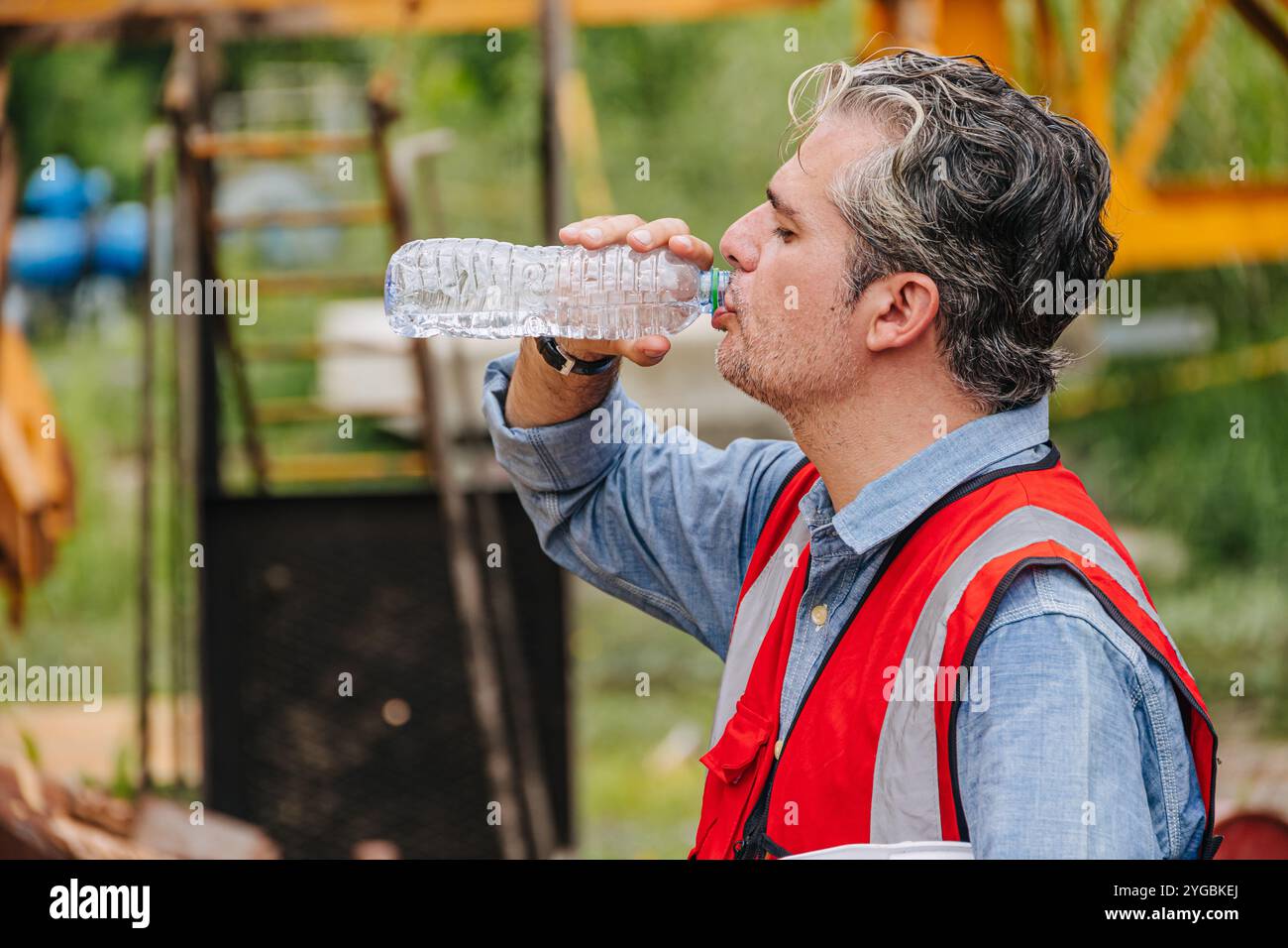 Construction worker in a hard hat and safety vest drinking water, staying hydrated during work ...