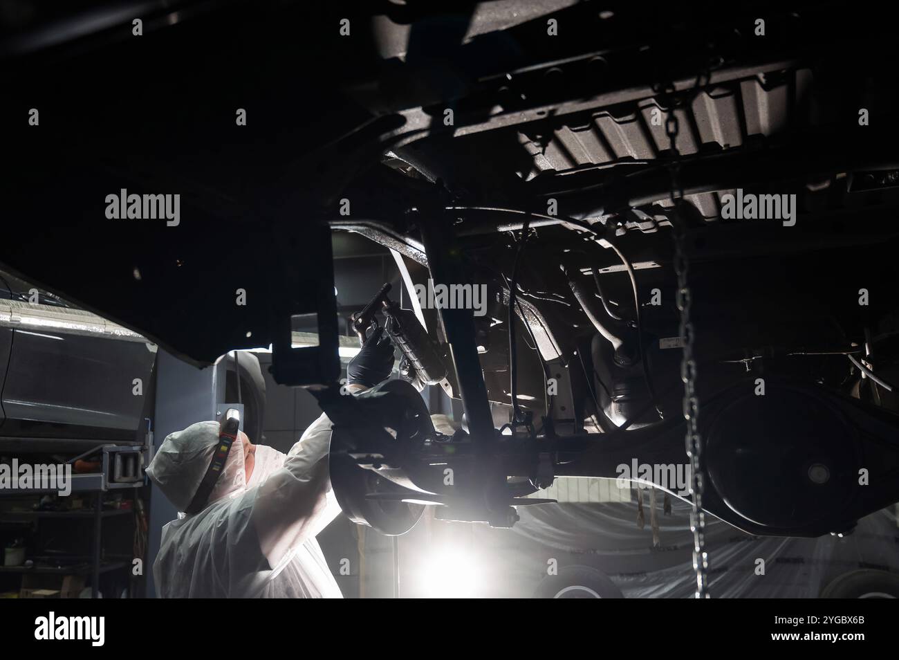 An auto mechanic applies anti-corrosion mastic to the underbody of a ...