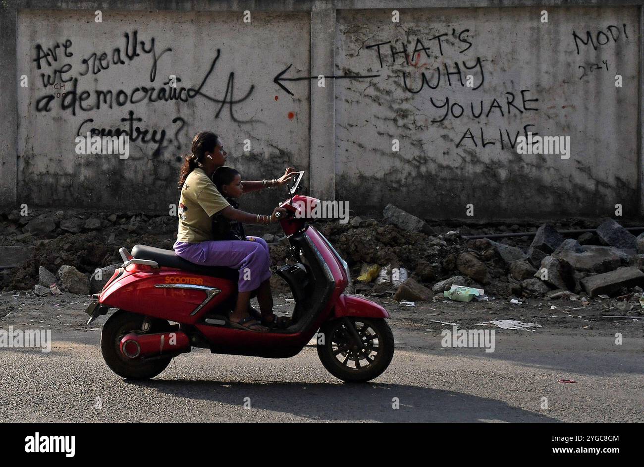 Daily life in Mumbai, India An Indian woman and child ride a scooter past graffiti messages ...