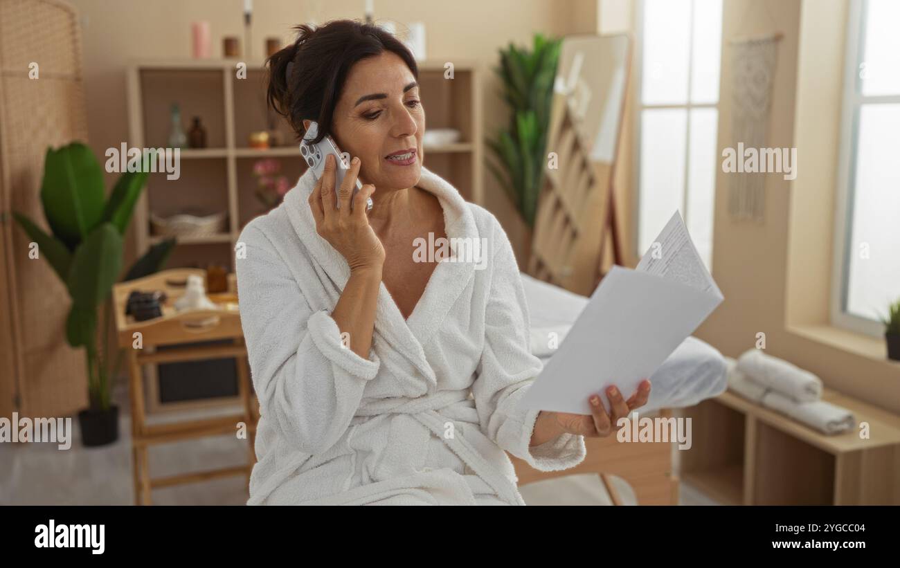 Woman talking on phone holding document wearing white robe in a spa ...