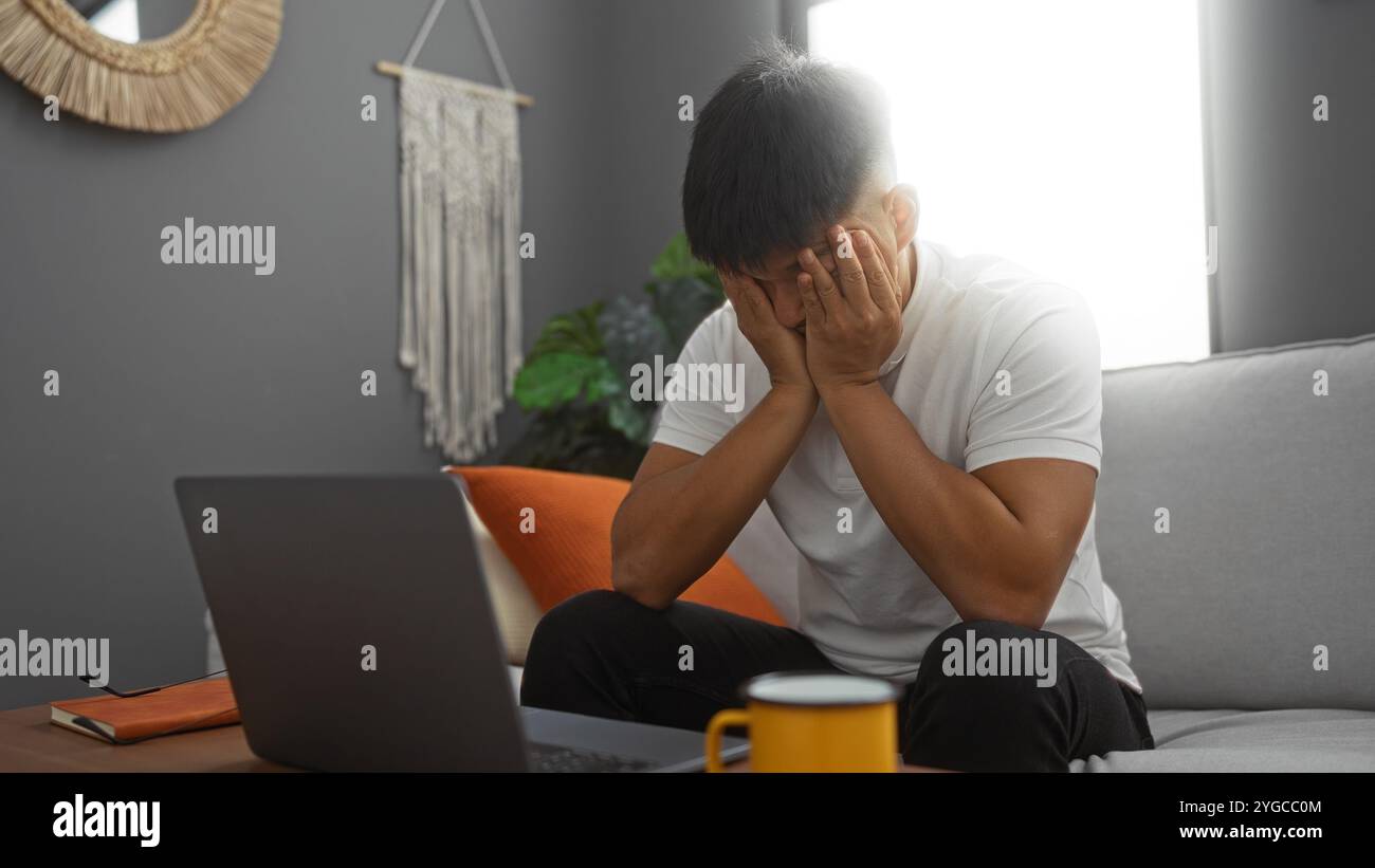 Man sitting in living room with laptop, looking stressed, indoors at ...