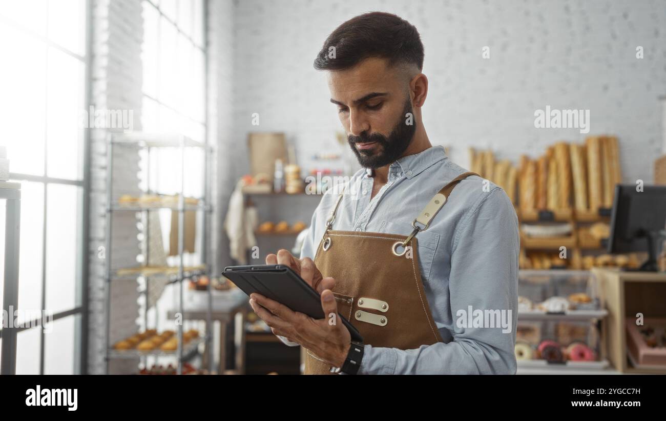 Handsome hispanic man with a beard wearing an apron and using a tablet ...