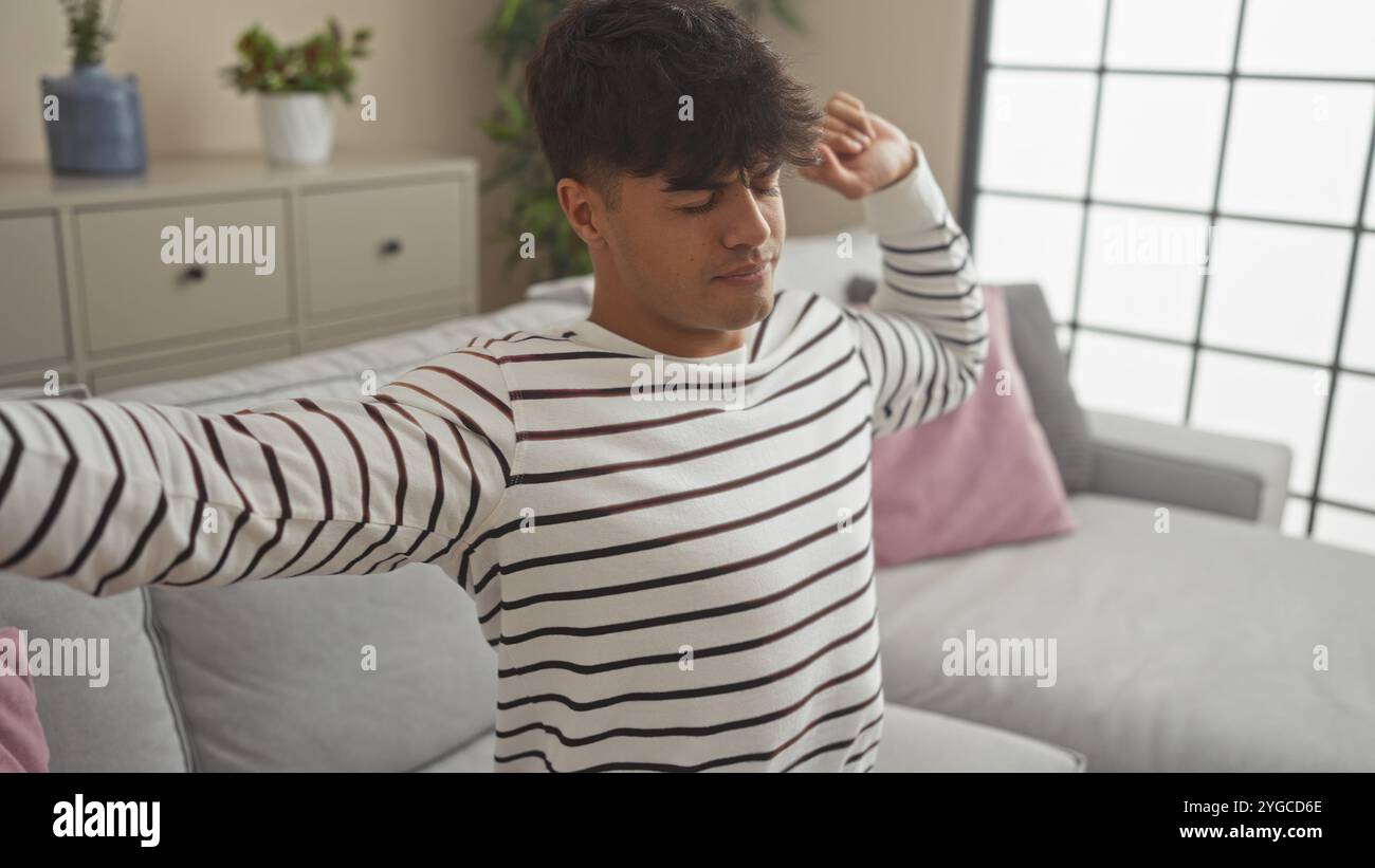 A handsome young hispanic man stretches in his living room, wearing a ...