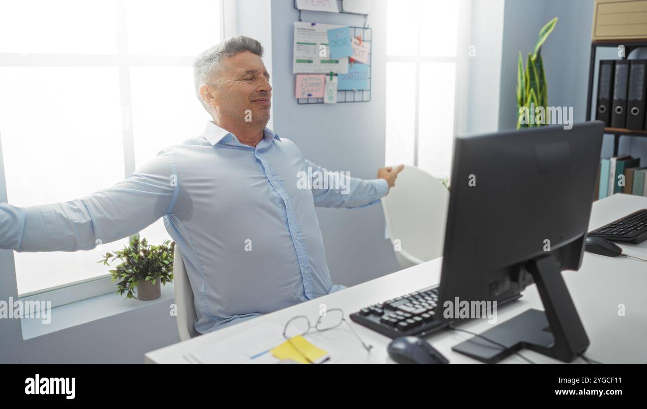 Middle-aged man stretching in an office with a computer monitor, indoor ...