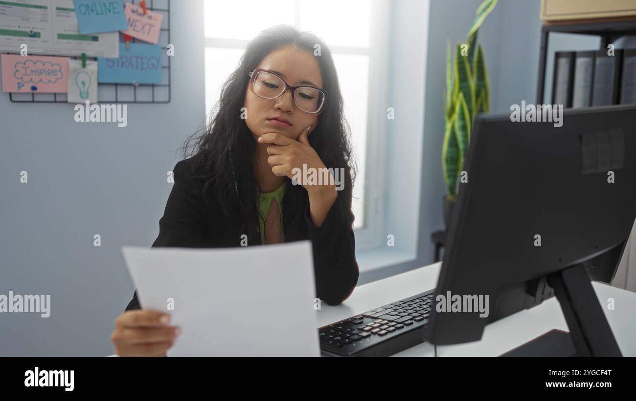 Woman thinking while reviewing document in modern office, with computer ...