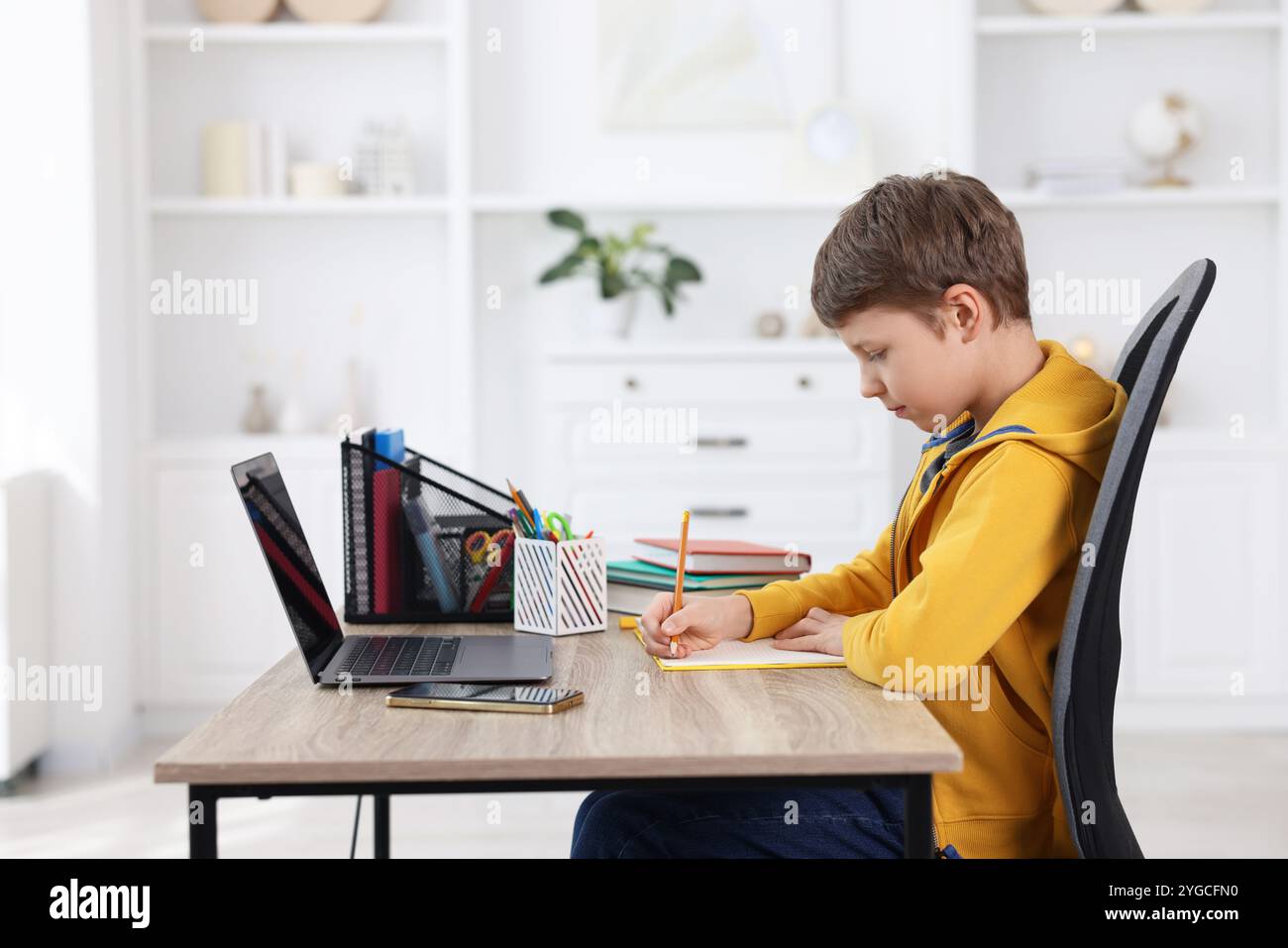 Boy with correct posture doing homework at wooden desk indoors Stock ...