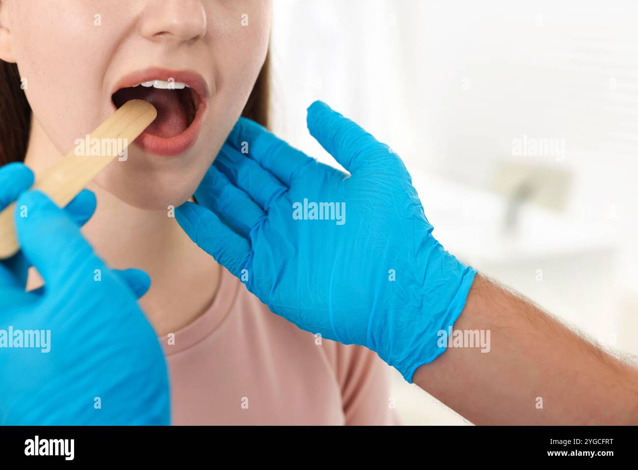 Doctor examining woman's throat with tongue depressor in clinic ...