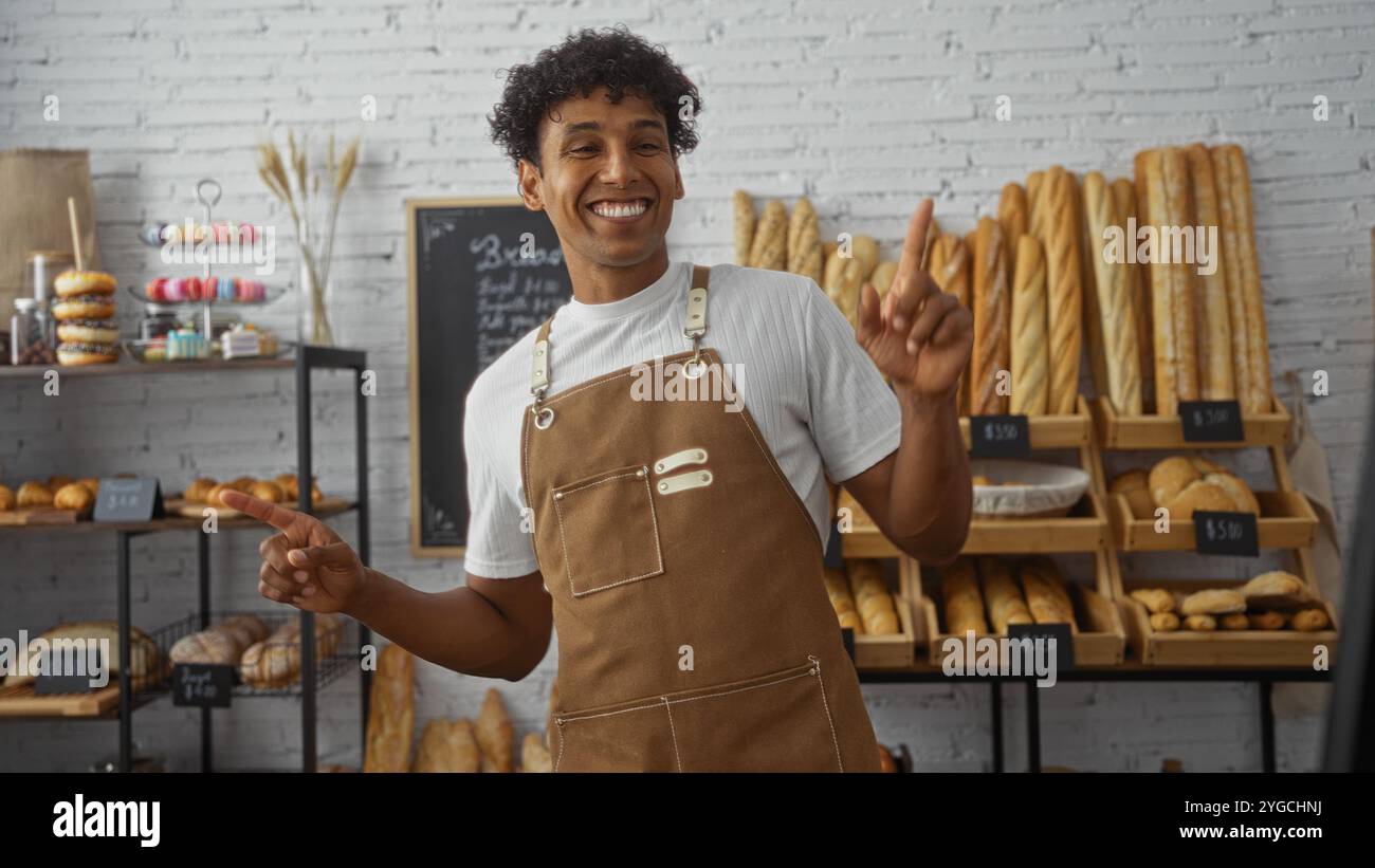 Young hispanic man smiling proudly inside a bakery shop wearing an ...
