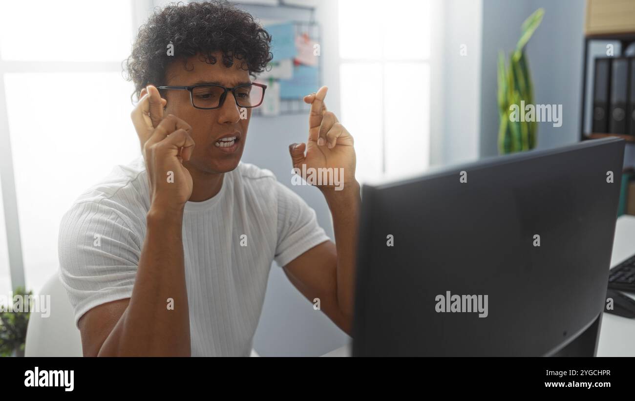 Young man in office crossing fingers in front of computer showing hope ...