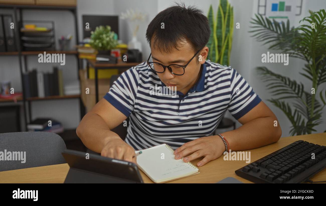 Young, asian man working intensely at his desk in a modern office ...