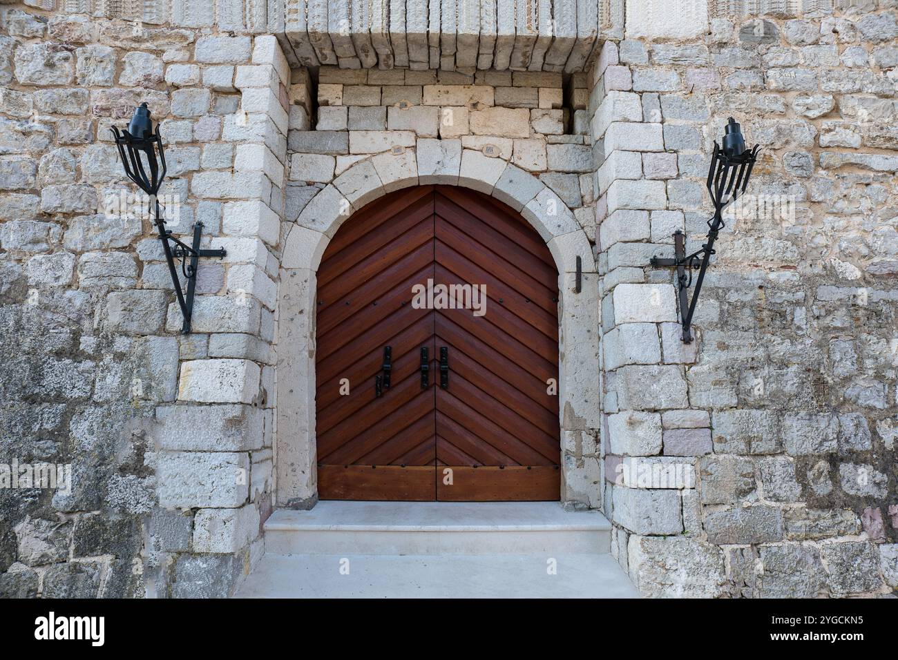 Wooden door on a Stone medieval house with torch holders on the sides ...