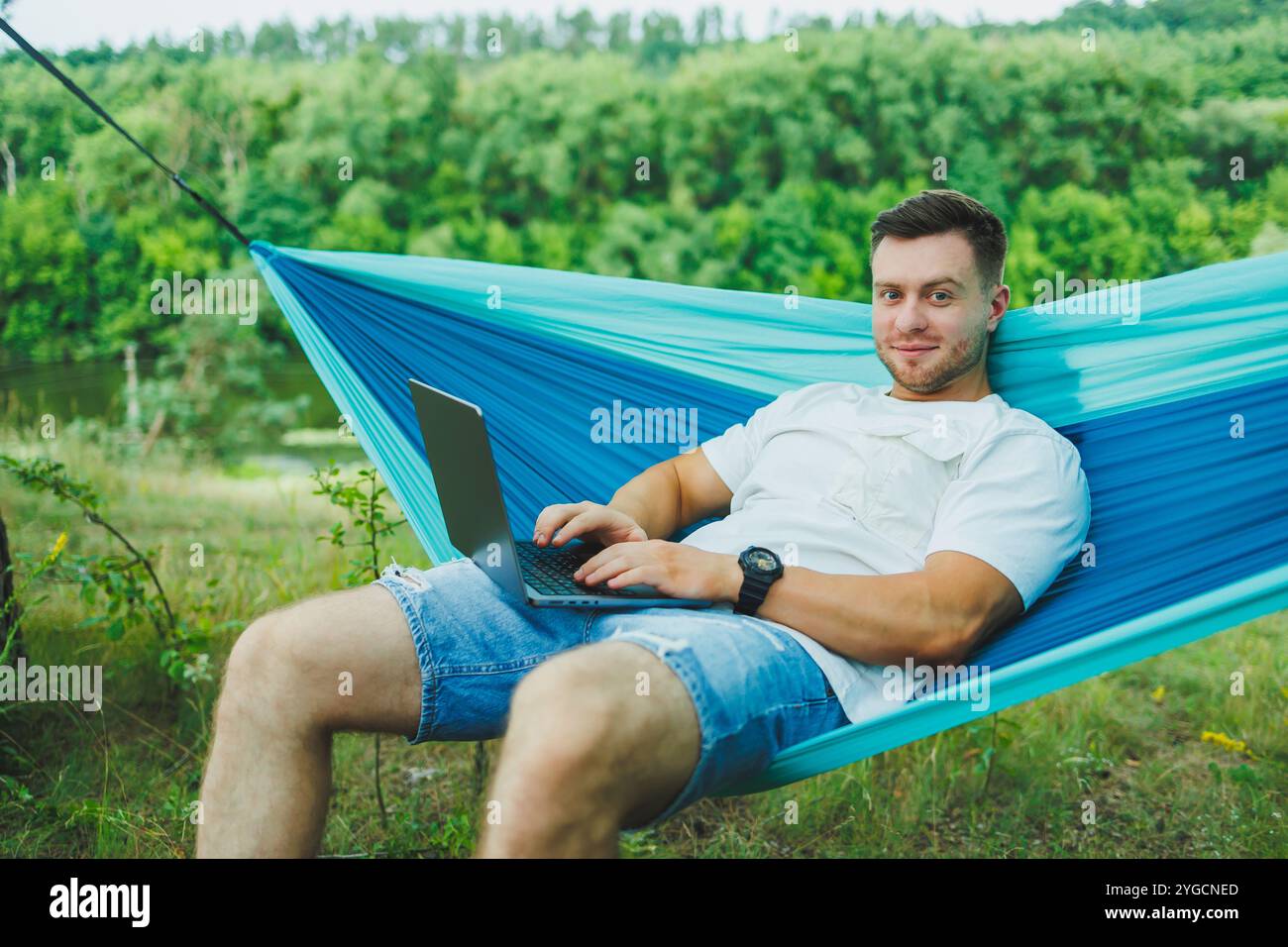 Handsome adult man relaxing in hammock while working on laptop during ...