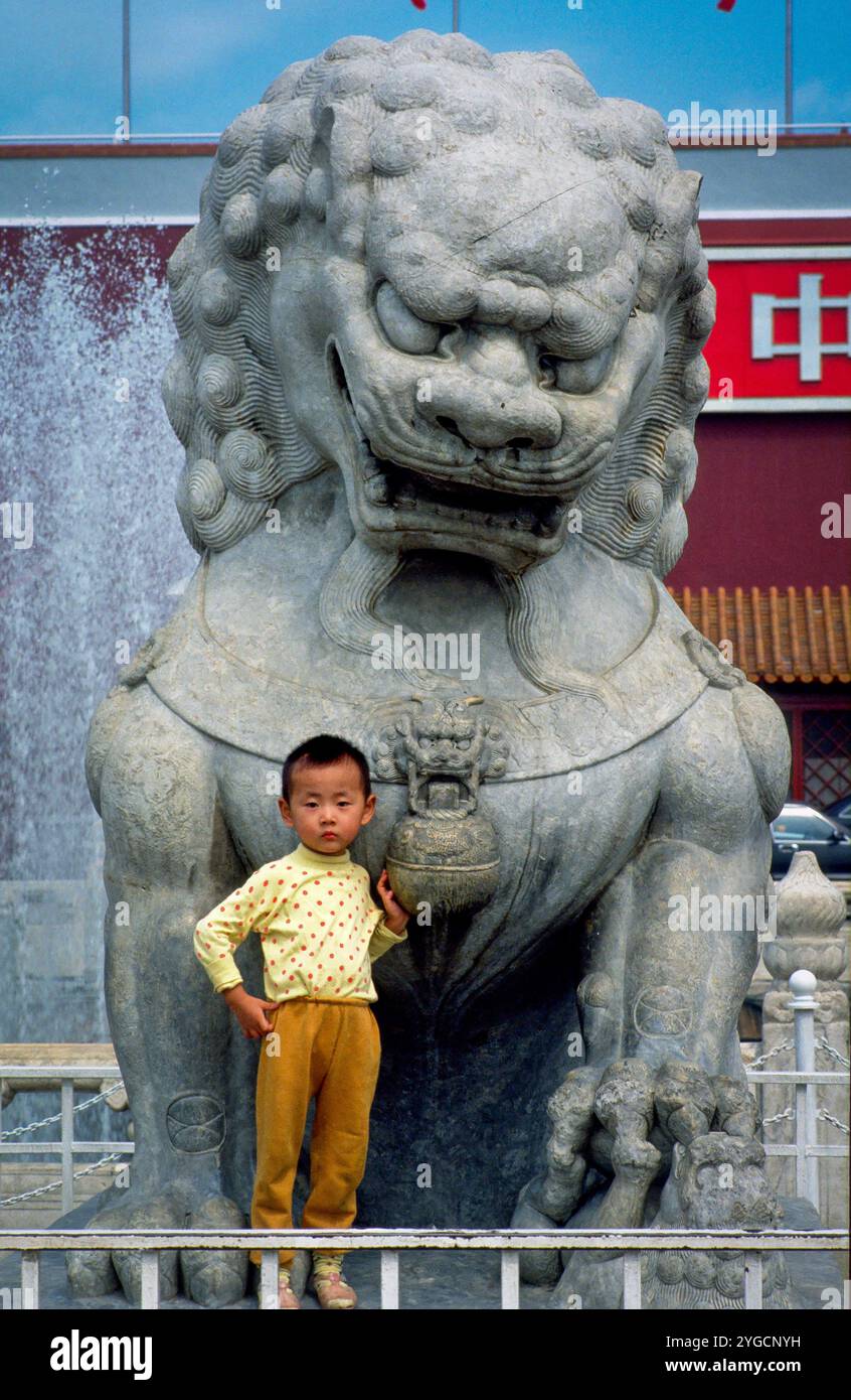 China, Beijing, boy is posing with a lion statue that guards the ...