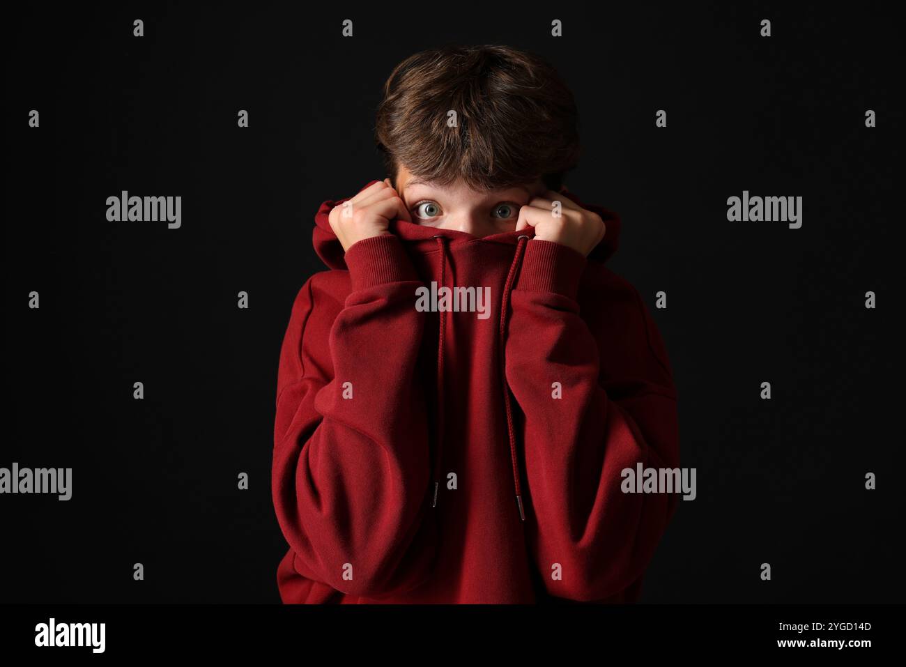 Scared teenage boy hiding on black background Stock Photo - Alamy