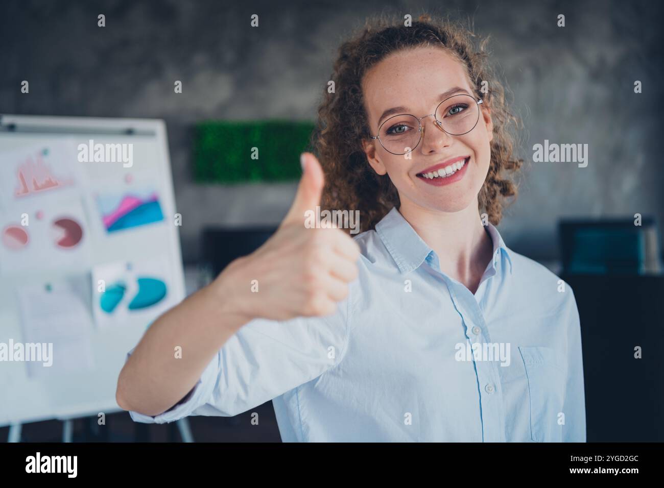 Confident young professional giving thumbs up at workplace, showcasing ...