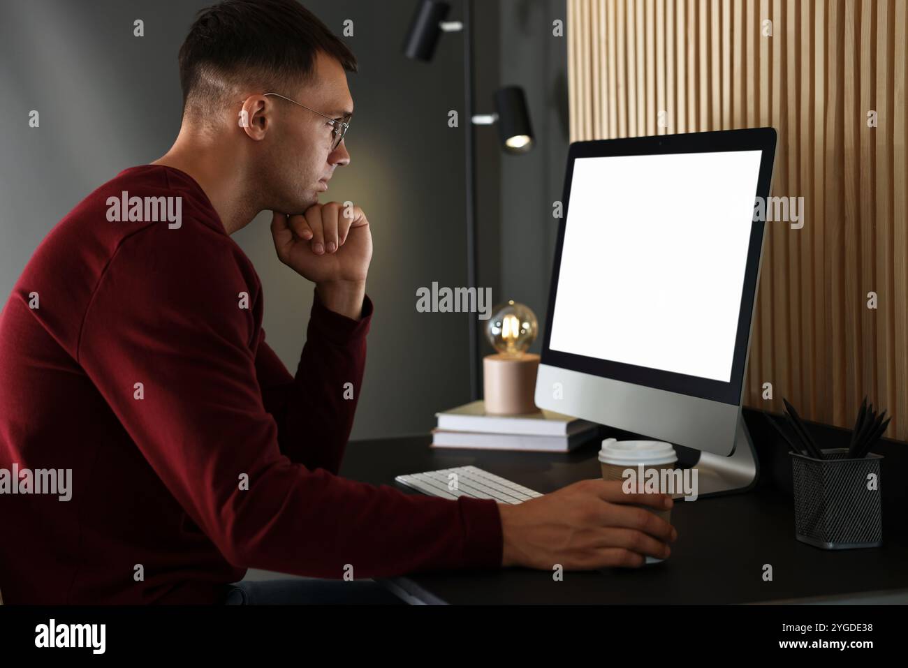 Man with drink using computer monitor at table indoors Stock Photo - Alamy