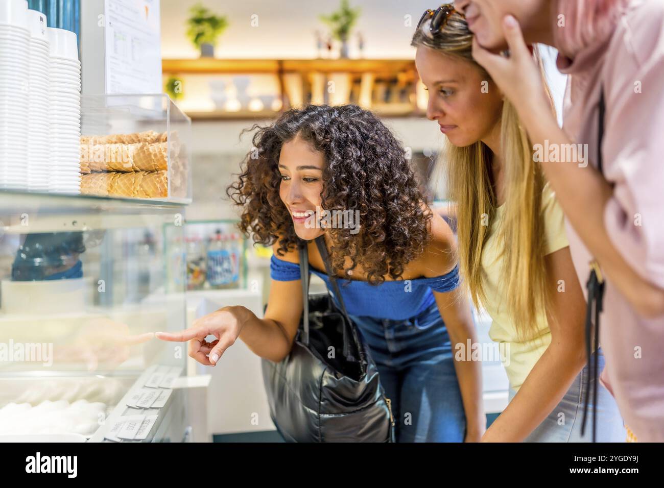 Happy friends buying ice cream in a shopping mall pointing to the glass ...