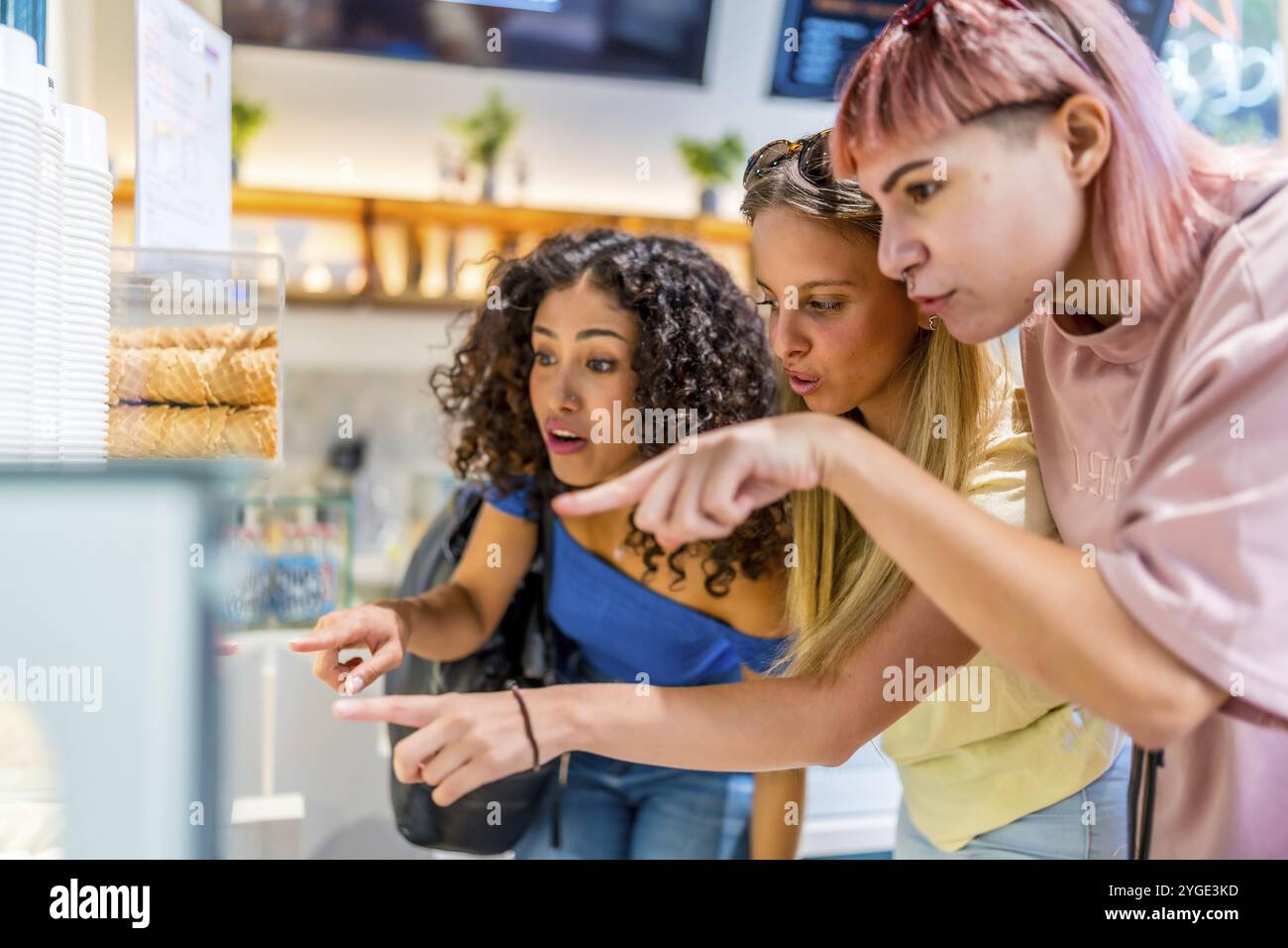 Side view of three diverse modern women pointing at ice cream glass ...
