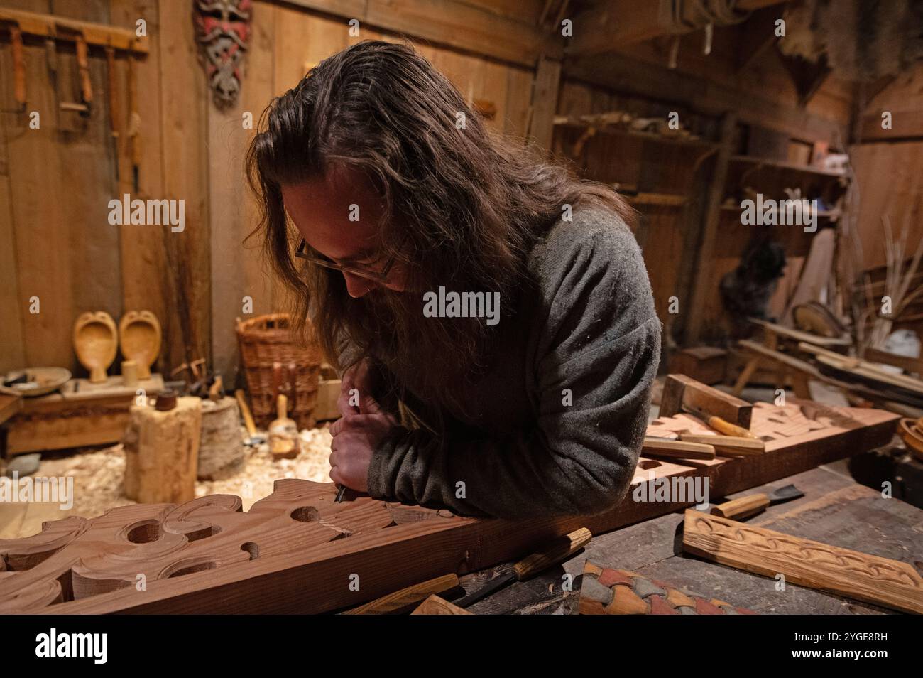 A Viking carpenter busy carving a long piece of wood to fit part of a ...