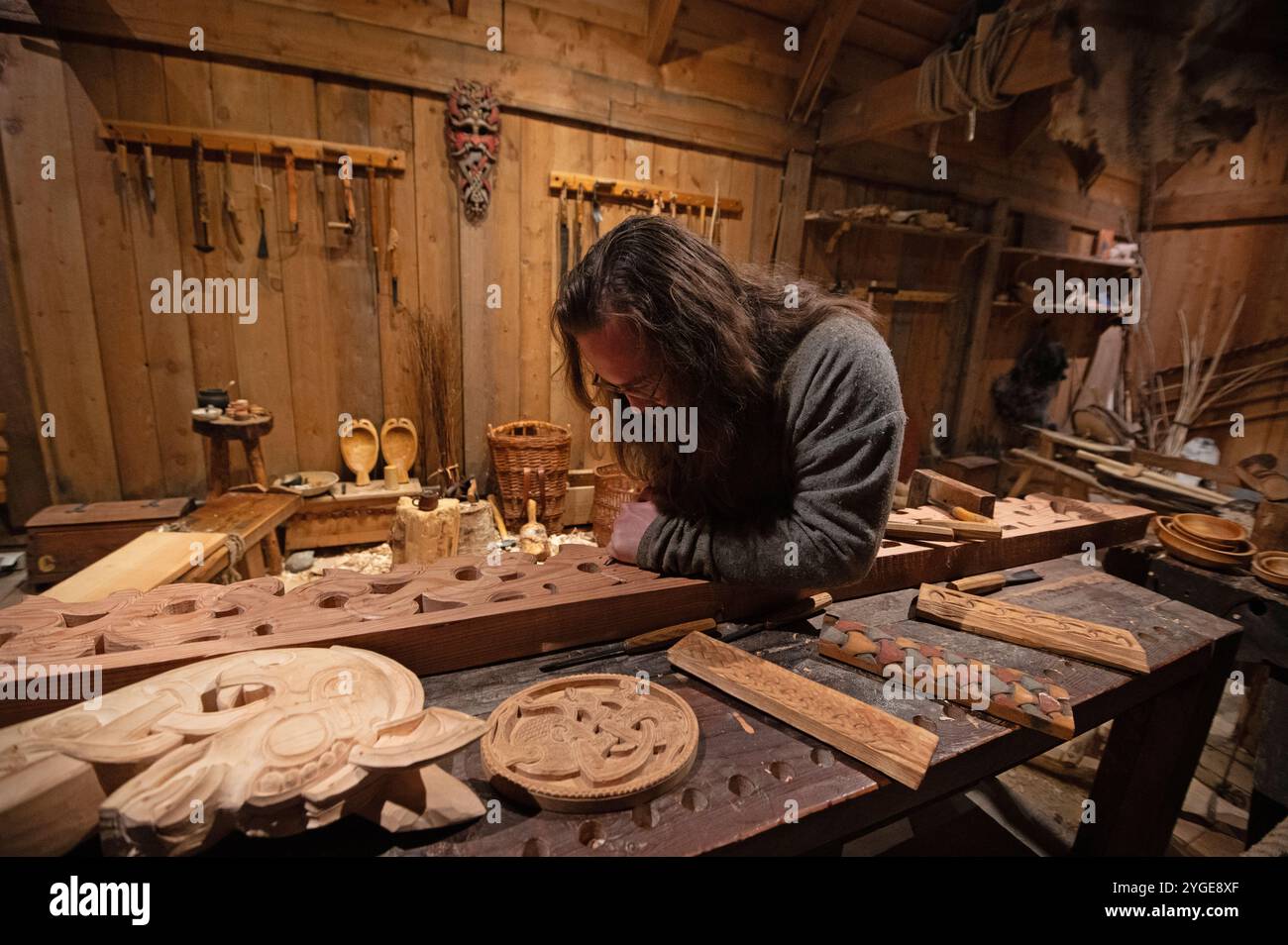 A Viking carpenter busy carving a long piece of wood to fit part of a ...