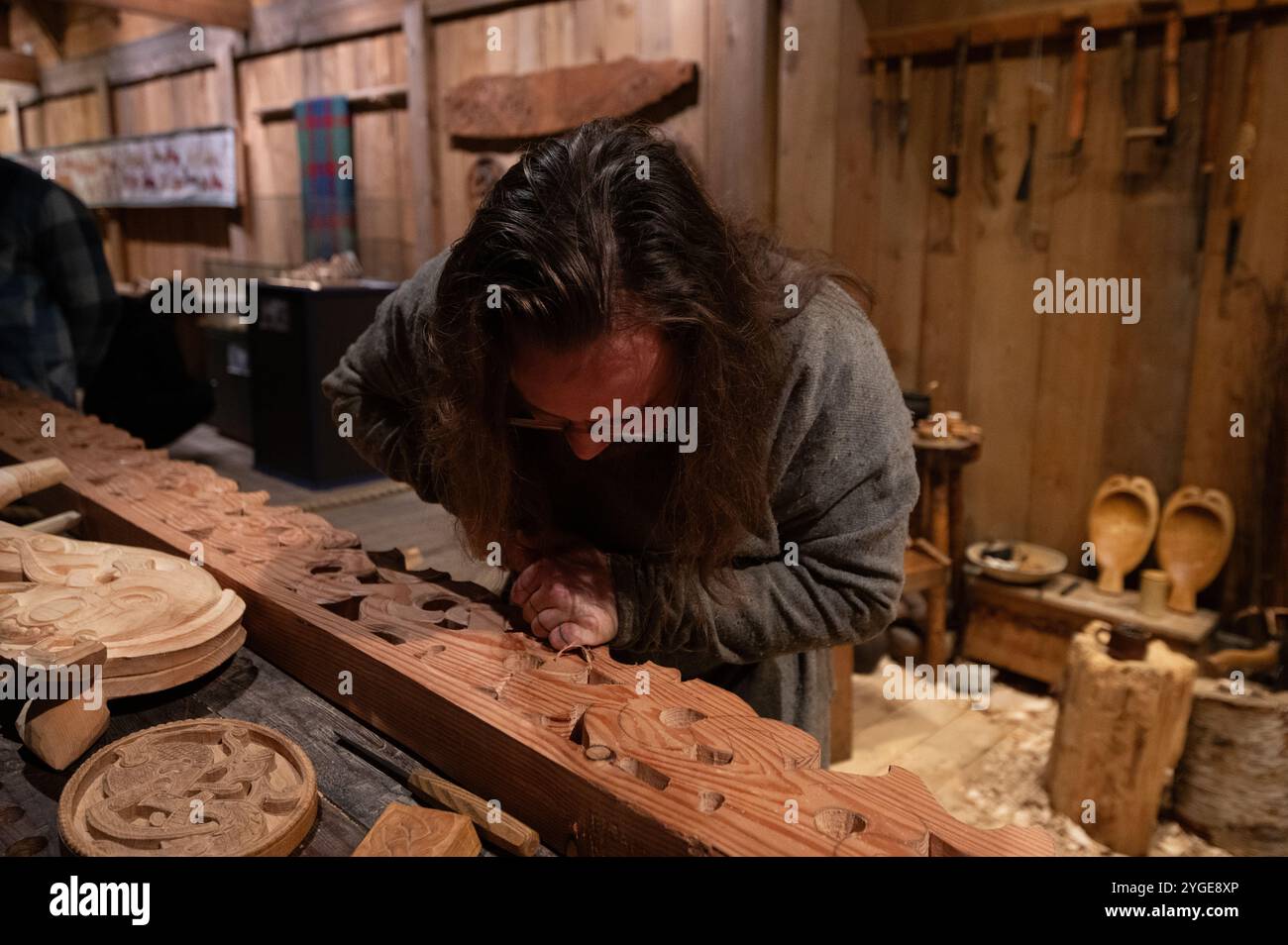 A Viking carpenter busy carving a long piece of wood to fit part of a ...