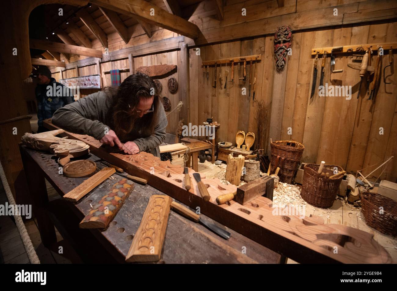 A Viking carpenter busy carving a long piece of wood to fit part of a ...