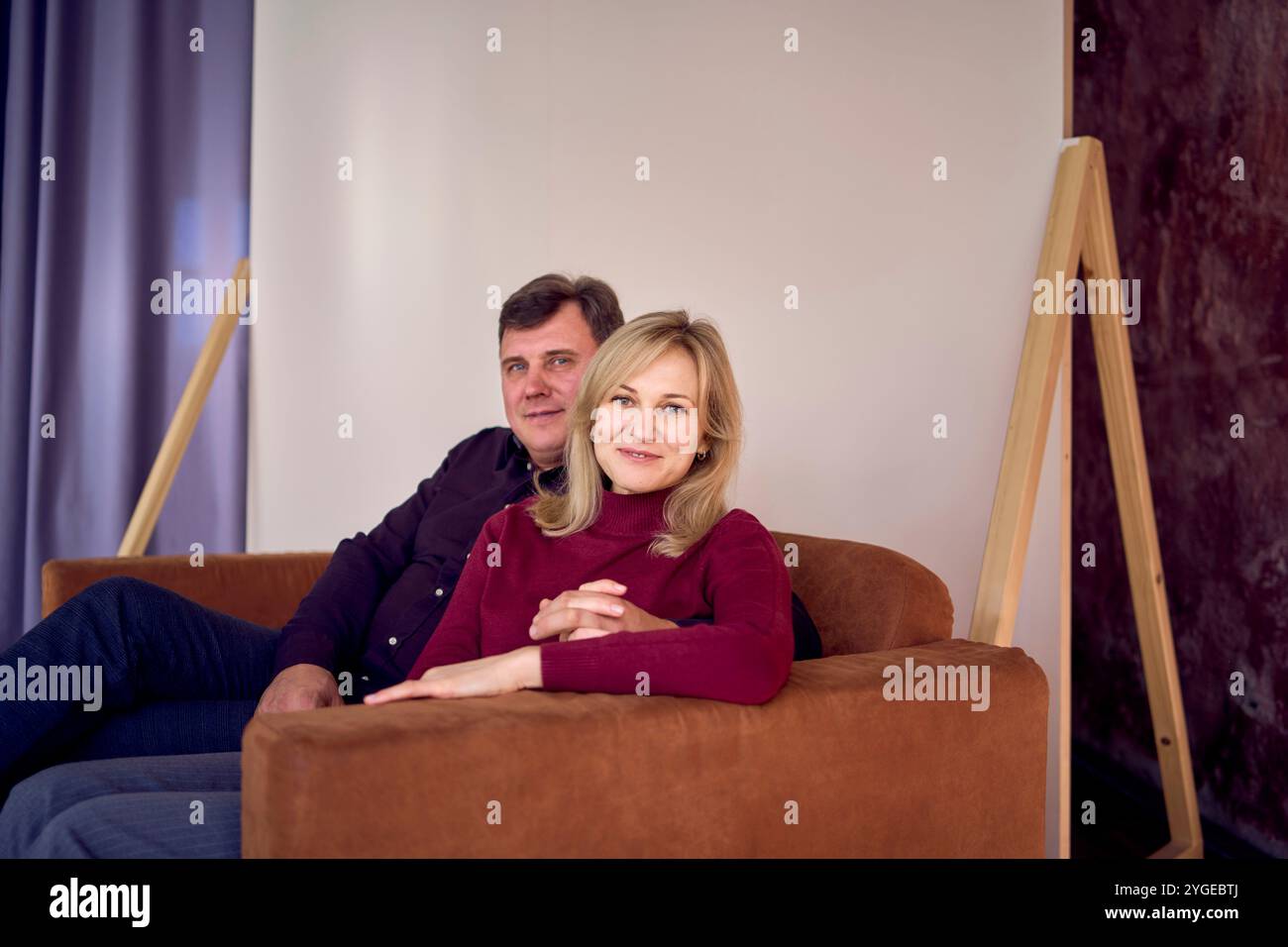 an attractive middle-aged married couple hugging and smiling on sofa ...