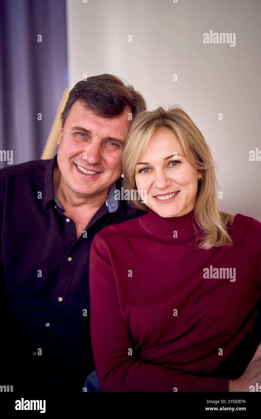 an attractive middle-aged married couple hugging and smiling on sofa ...