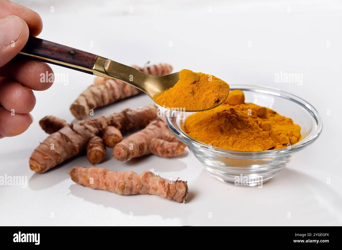 Turmeric powder in a bowl and turmeric root, hand holding a spoon and ...