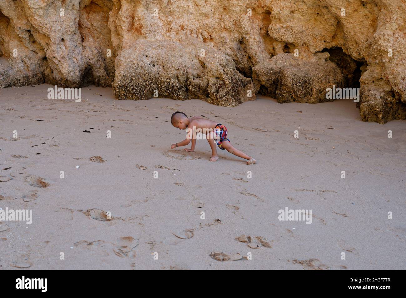 Young boy focused on drawing in the sand at praia da rocha, enjoying a ...