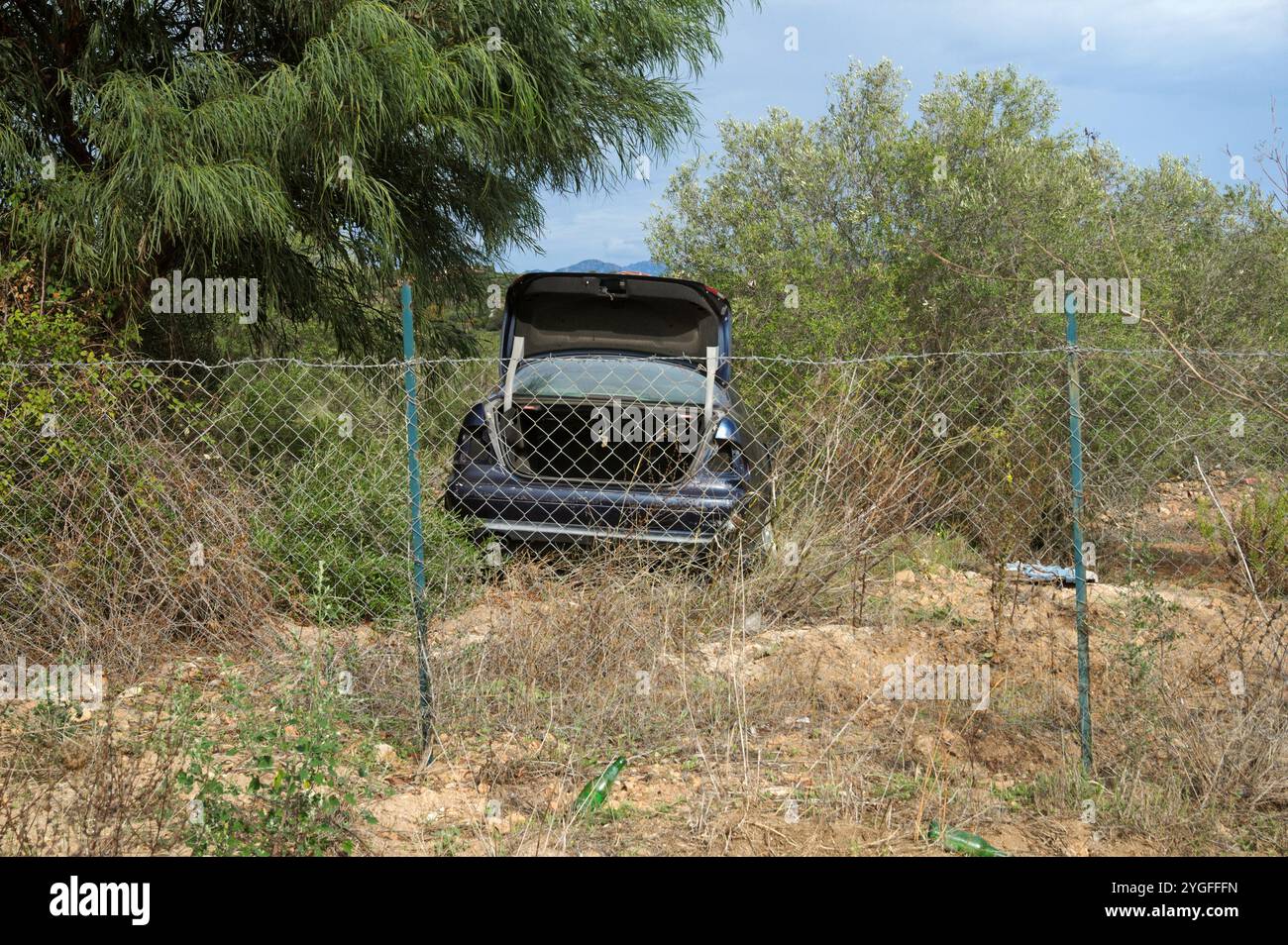 abandoned car with open trunk behind a fencing net Stock Photo - Alamy