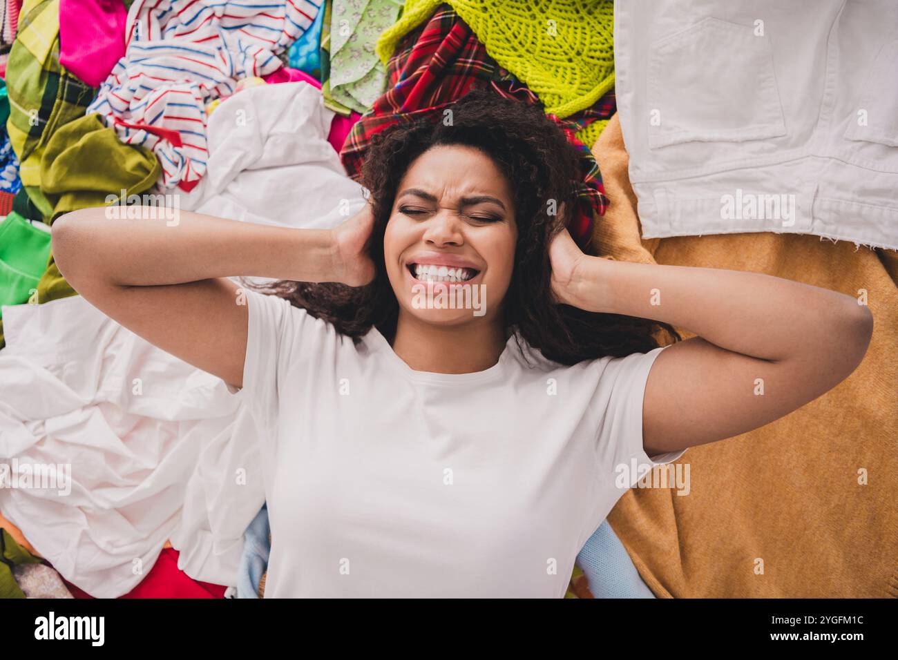 Joyful young woman lying amidst colorful clothes heap, embracing ...