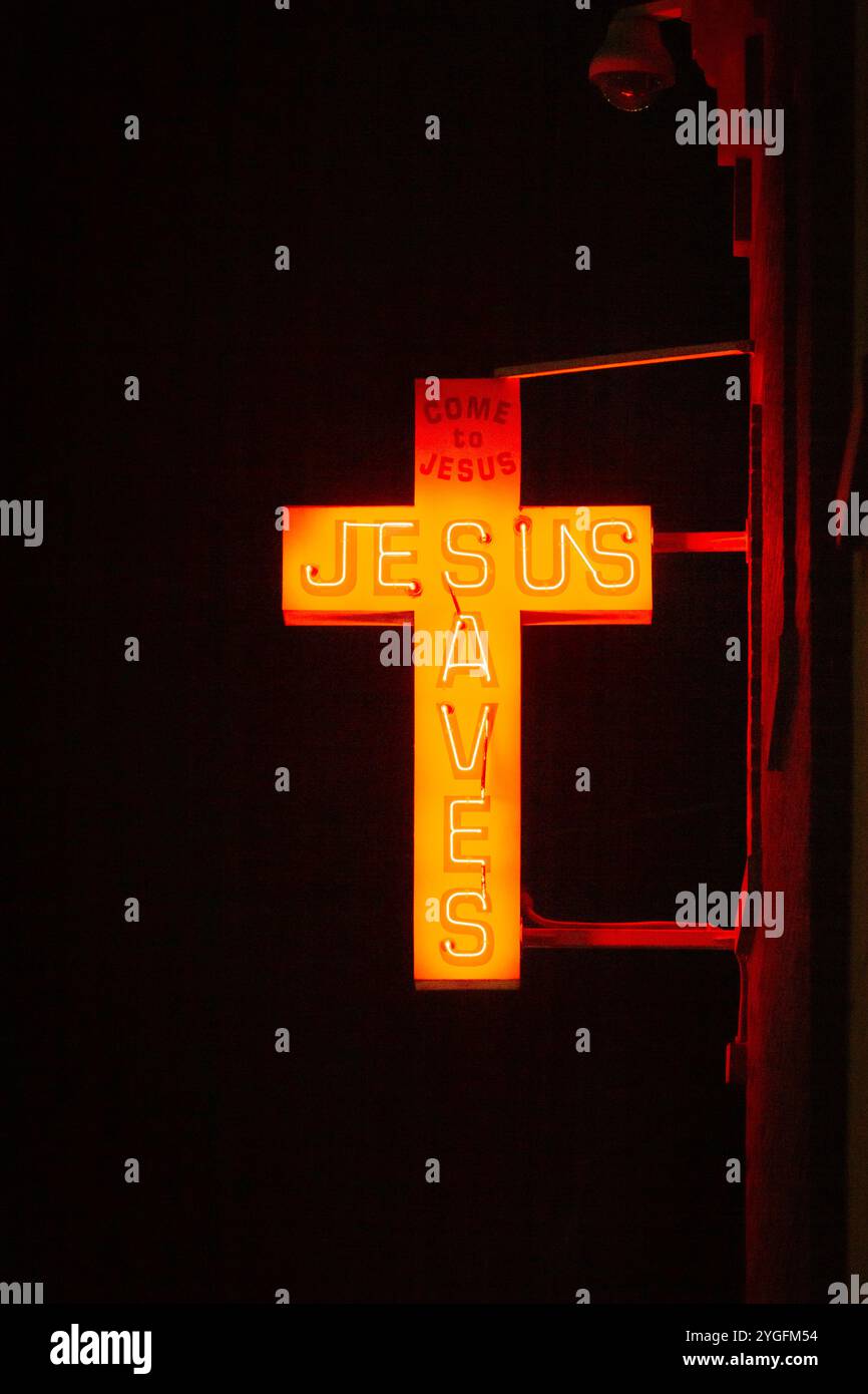 neon sign in the shape of a cross with the words Jesus Saves glows in a ...