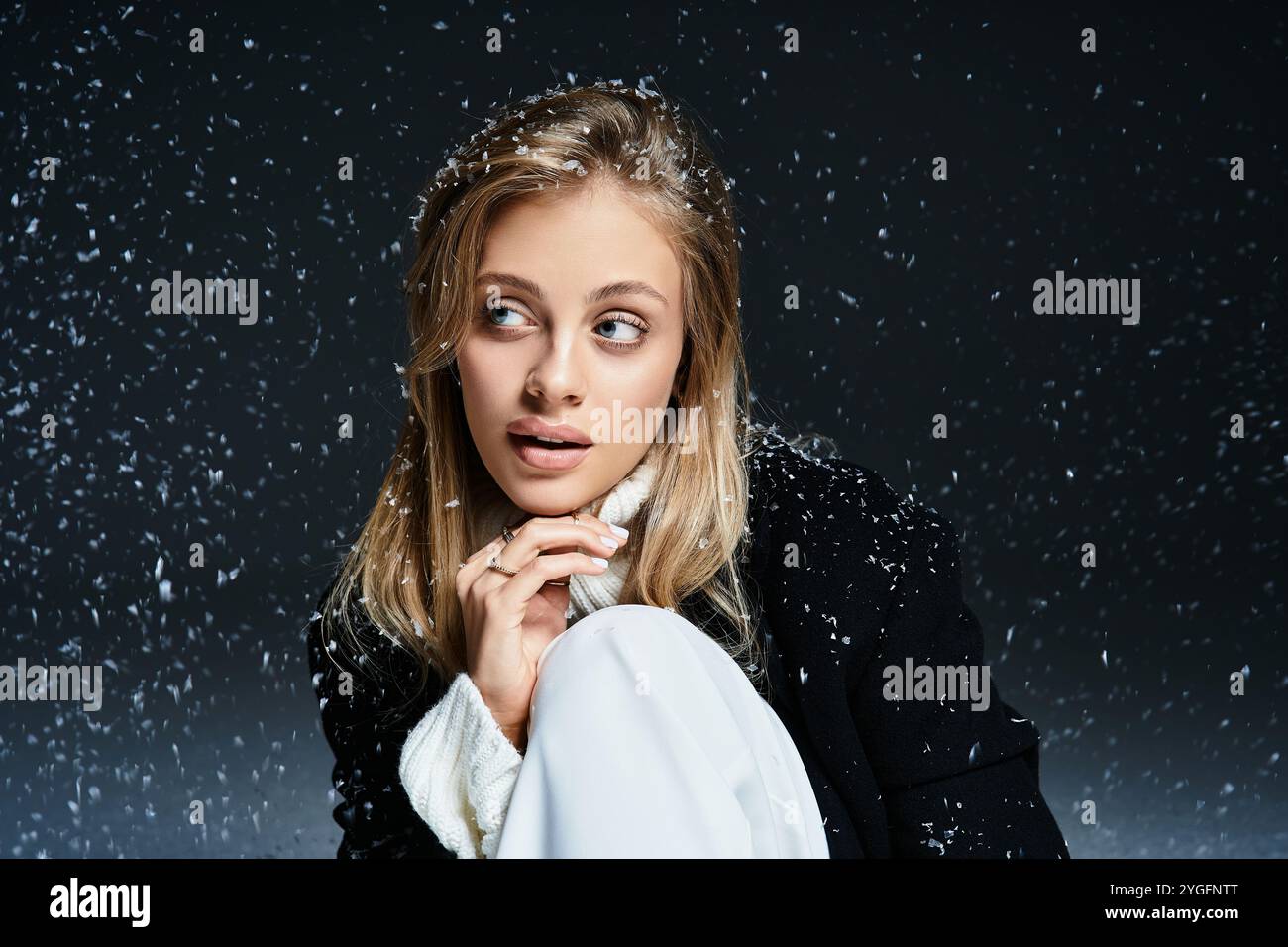 A beautiful young woman gazes thoughtfully as snow gently falls around her in the dark Stock ...
