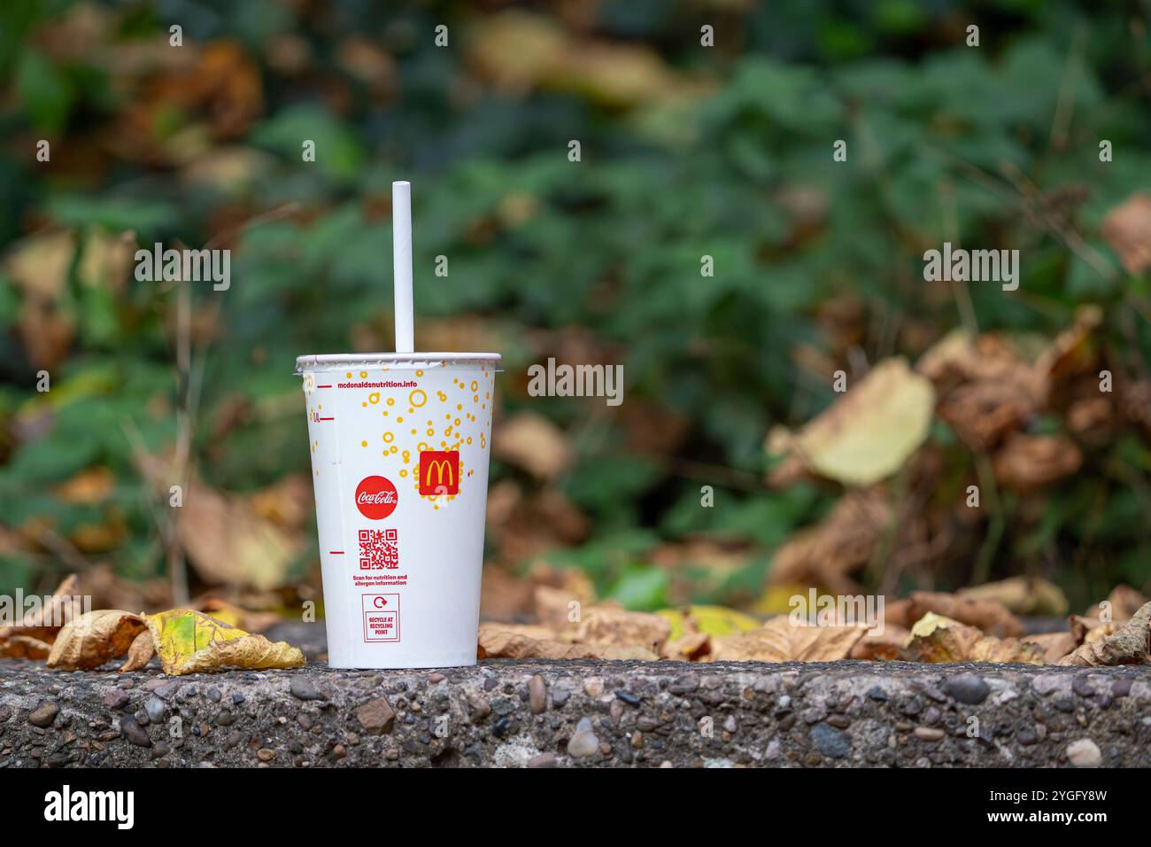 Disused Mcdonalds paper cup with straw discarded on an outside stone ...