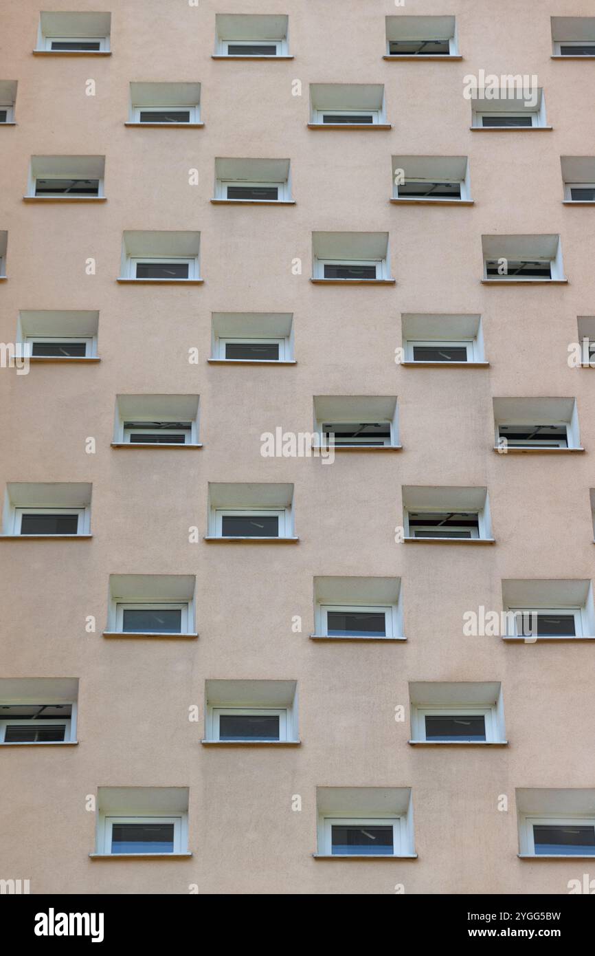 A beige building facade with small, uniformly arranged square windows ...