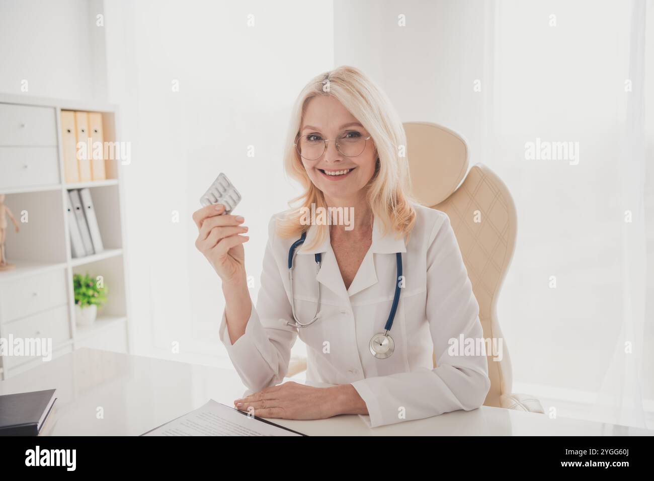 Mature female doctor in clinic office holding medication pack ...
