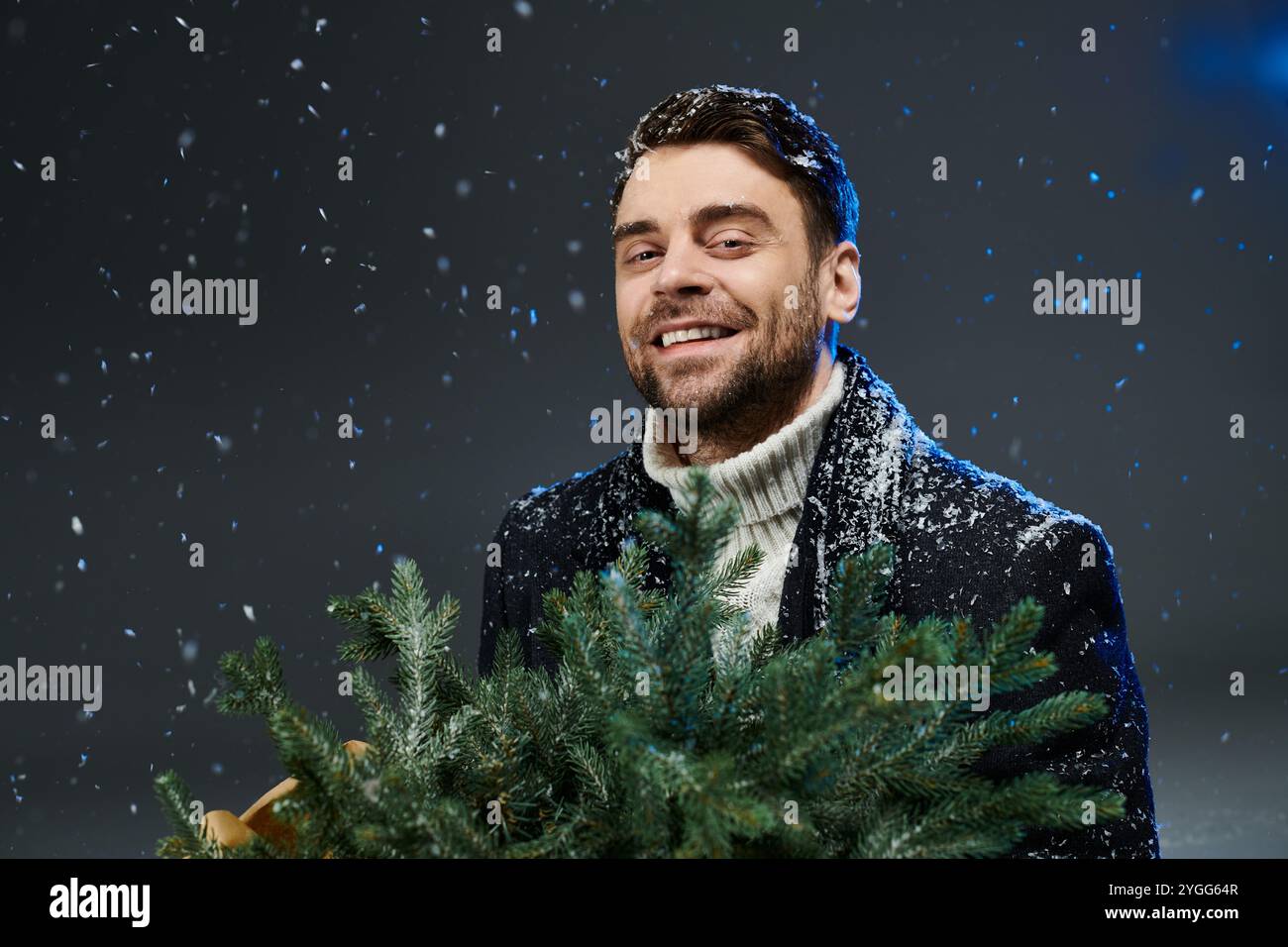 A young man enjoys a snowy moment, holding fresh evergreen branches ...