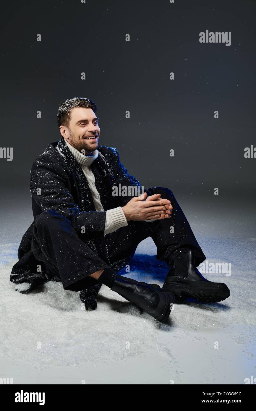 The young man in snowy attire sits in delight, embracing the winter ...