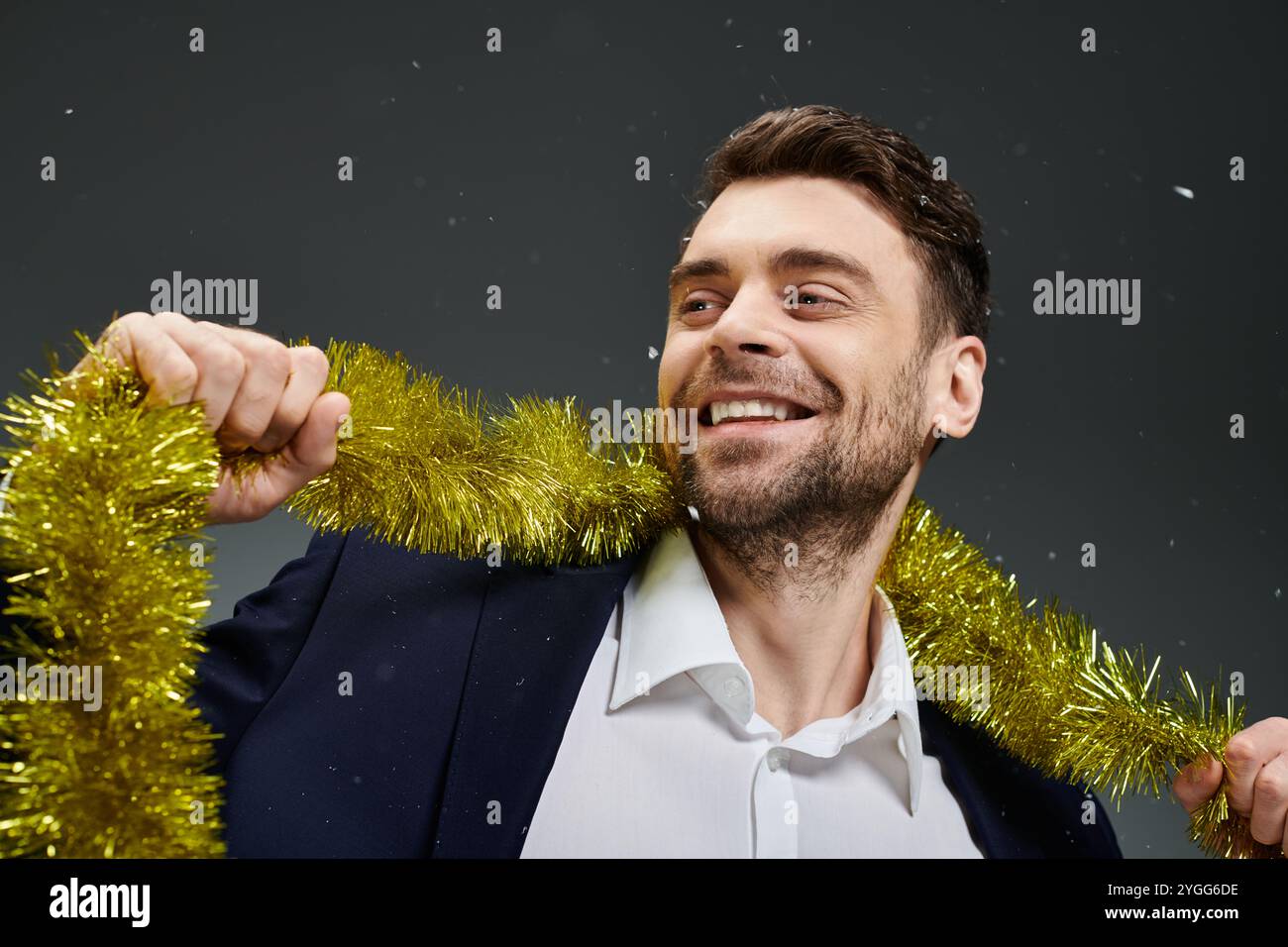 A handsome young man smiles brightly while holding shimmering tinsel on ...